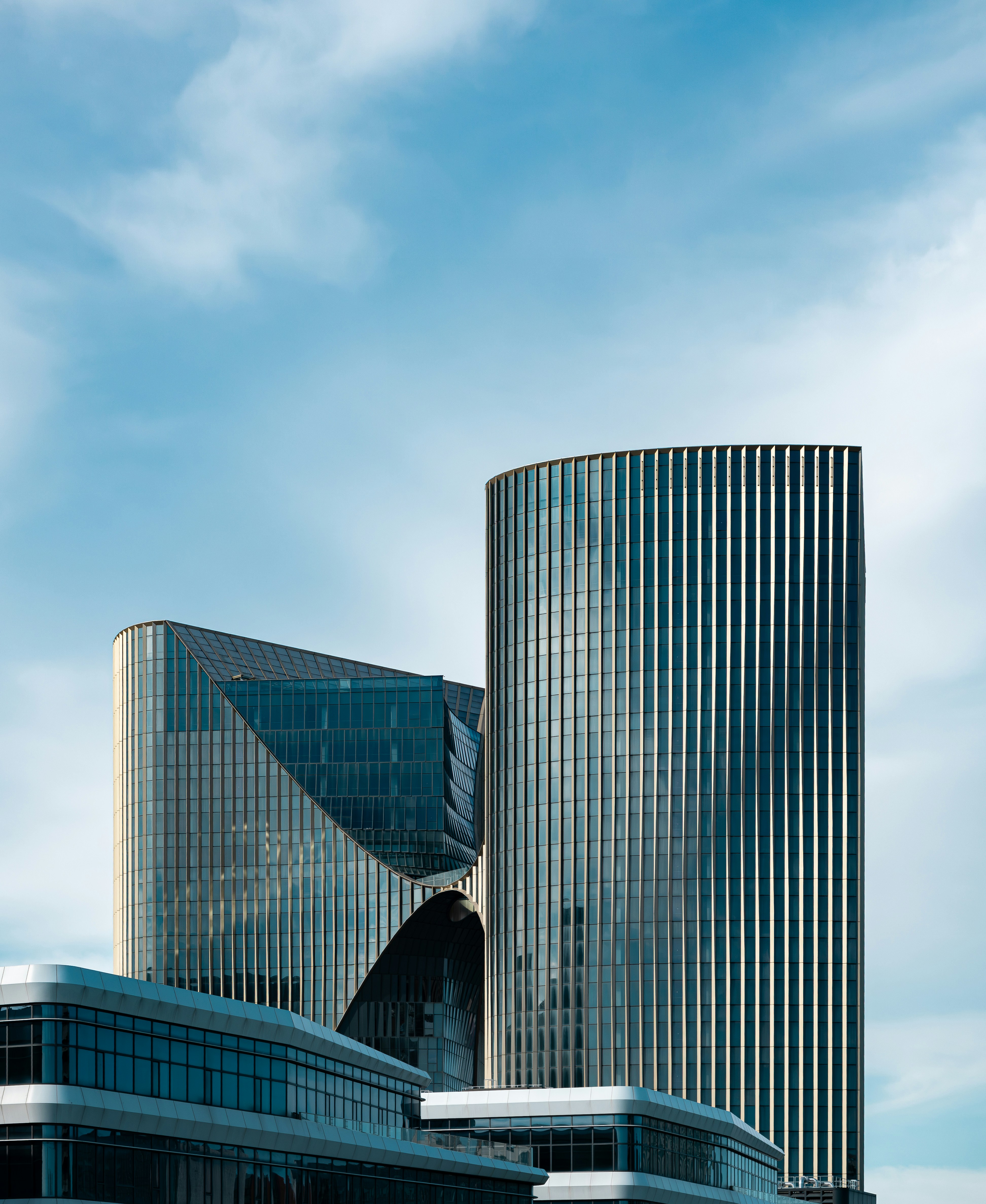 Modern glass-clad towers rise against a blue sky, their curved and angular facades creating a dynamic architectural silhouette.