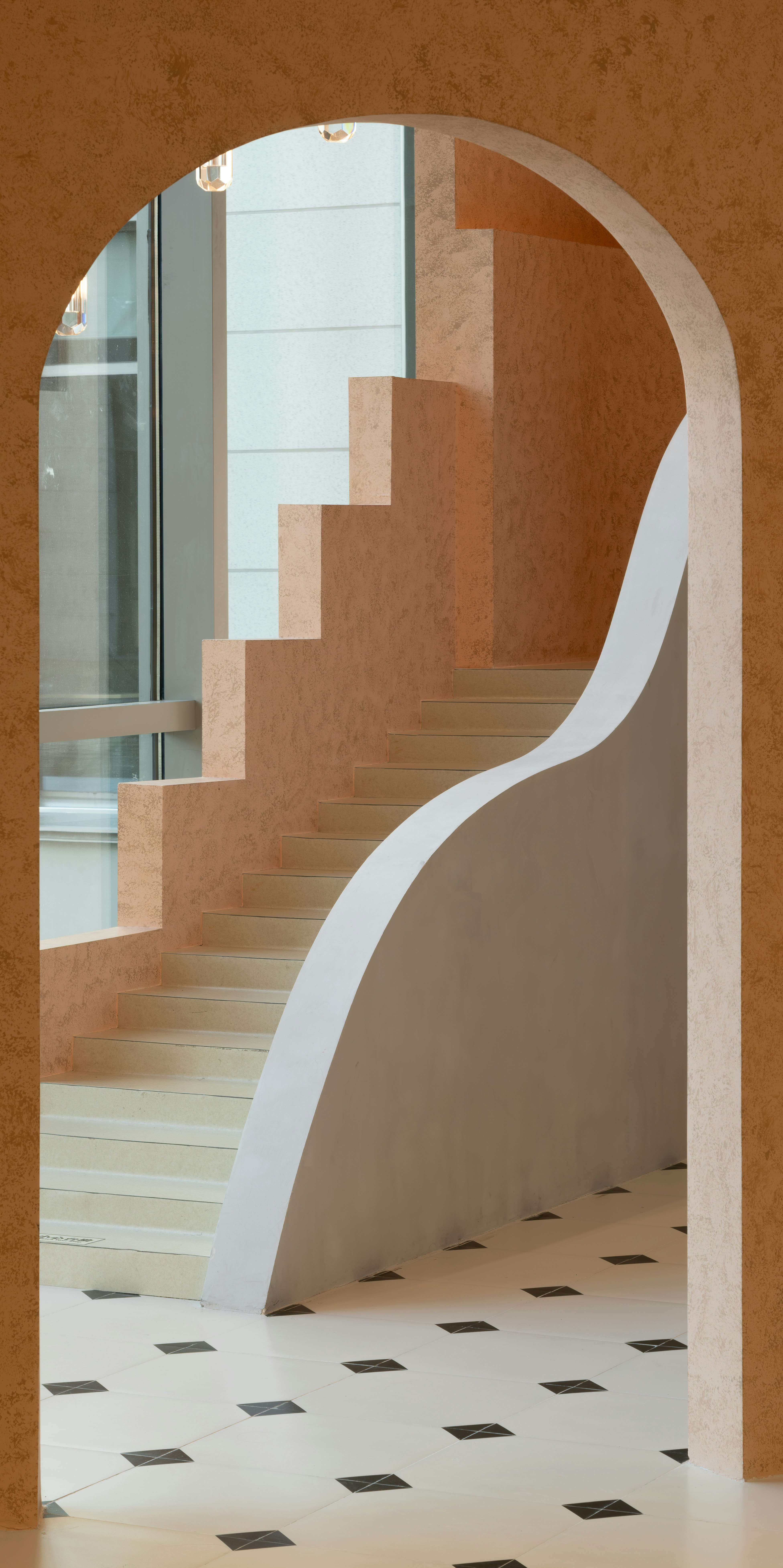 Architectural stairwell framed by a curved white railing within a warm orange arch, bathed in natural light from a window. The image emphasizes geometry and depth of the interior space.