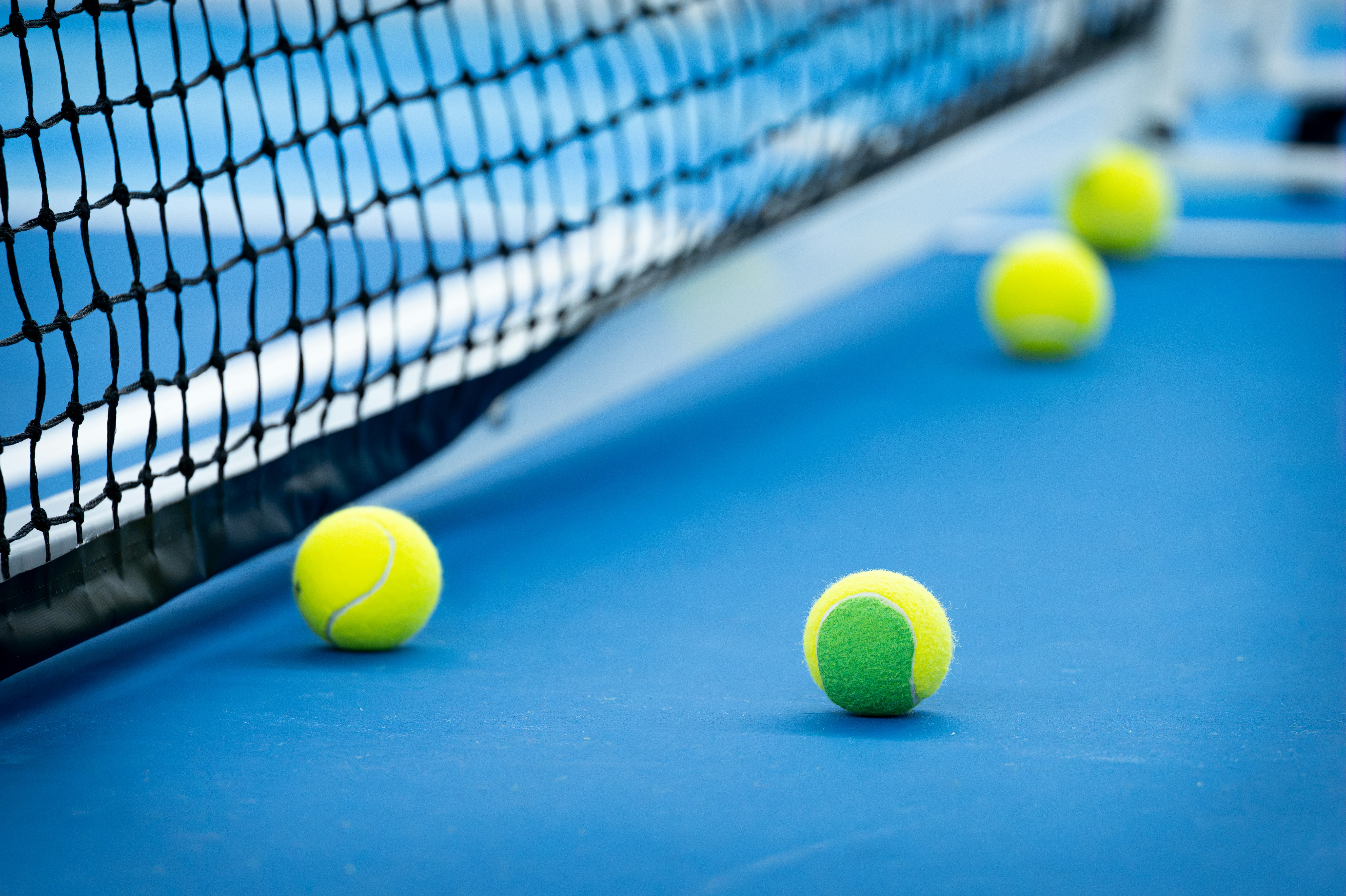 Bright Yellow Tennis Balls Scatter Across a Blue Court Under a Net