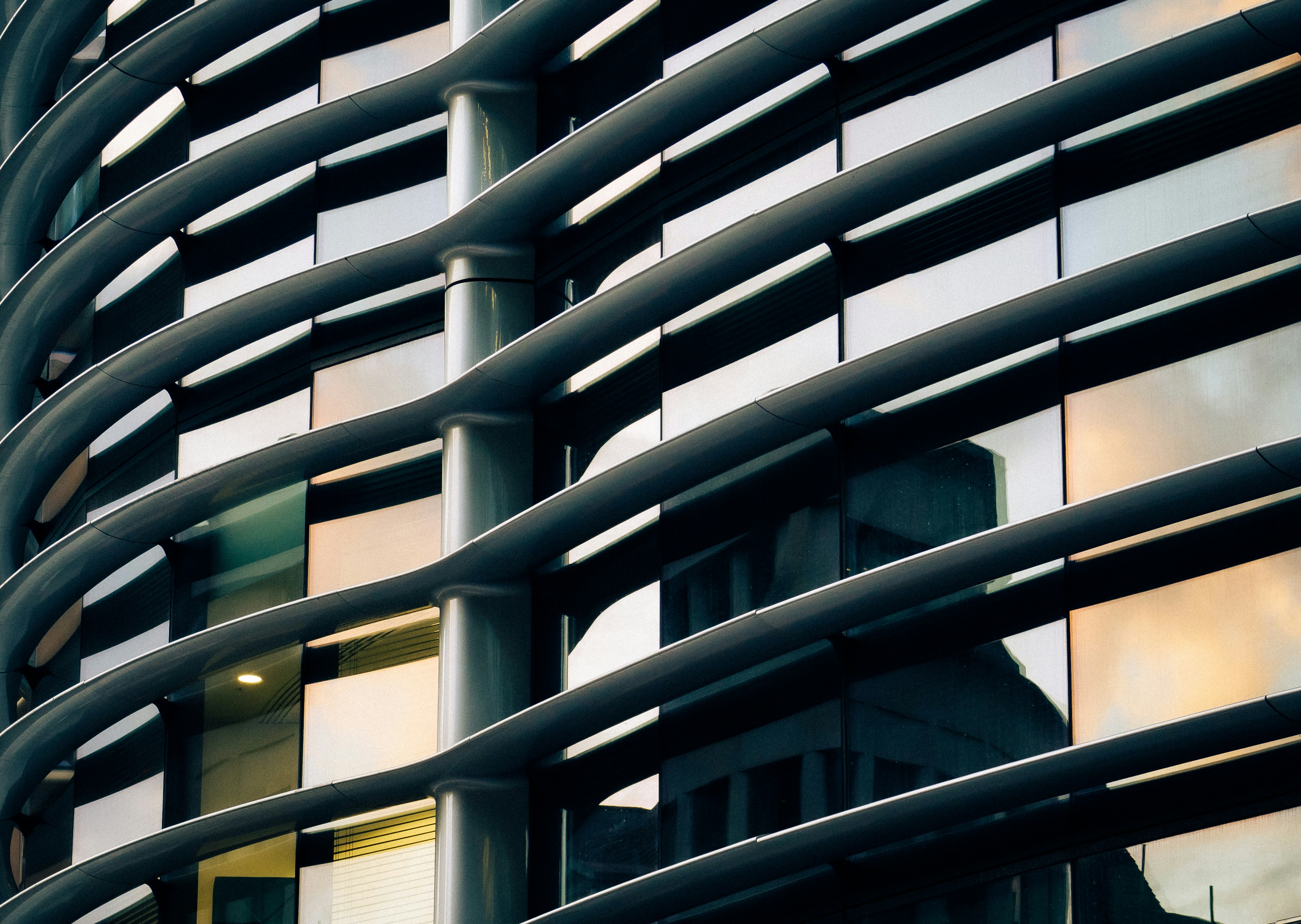 Reflective glass facade with curved horizontal bars creating a geometric pattern and subtle color reflections.
