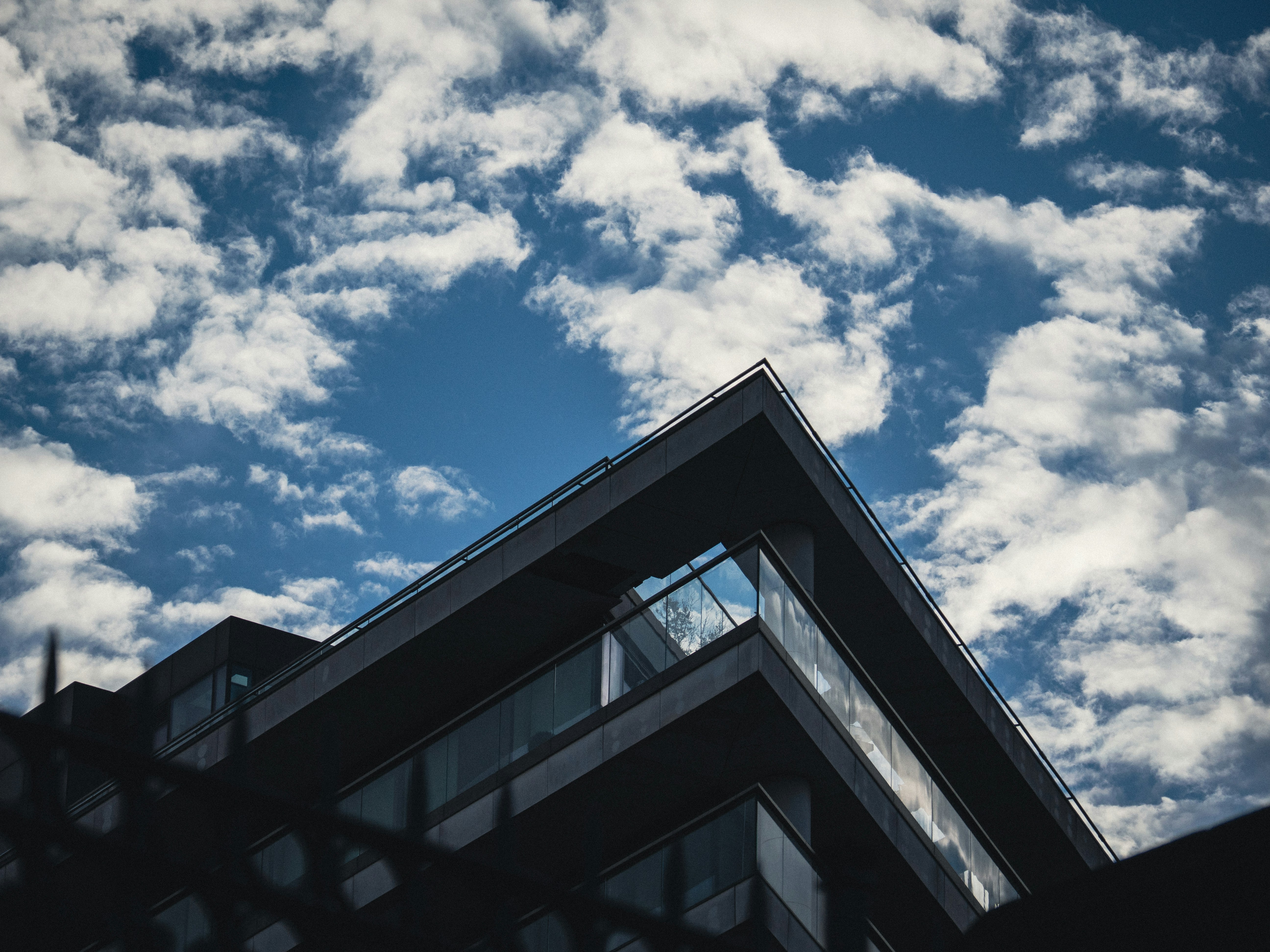 City rooftop corner with glass balconies against a blue sky; architectural details and shadows define the scene.