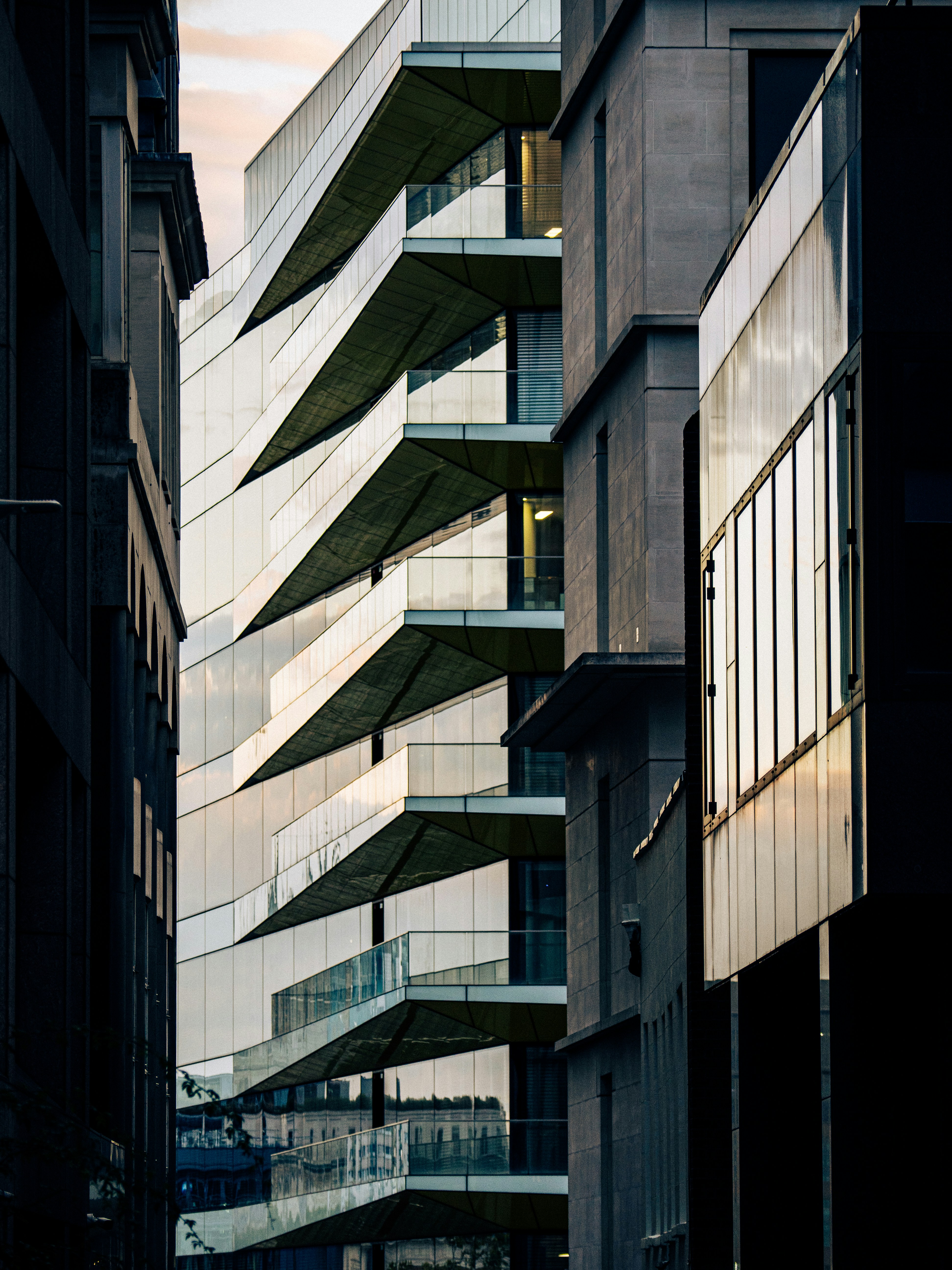 Vertical cityscape showcasing diagonal cantilever balconies between dark building facades; glass reflections and warm light emphasize architectural rhythm.