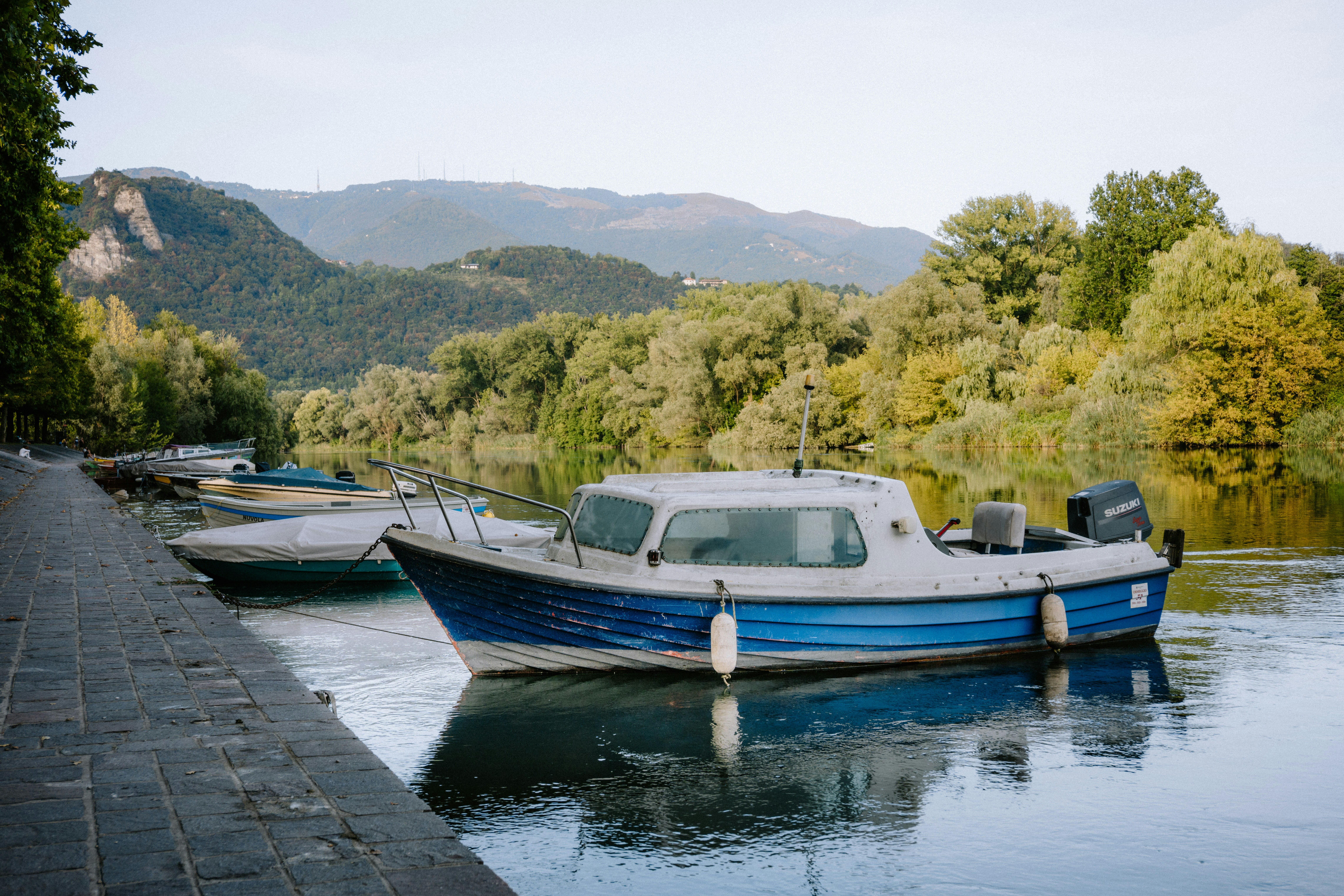 A blue and white motorboat moored along a stone embankment on a calm river