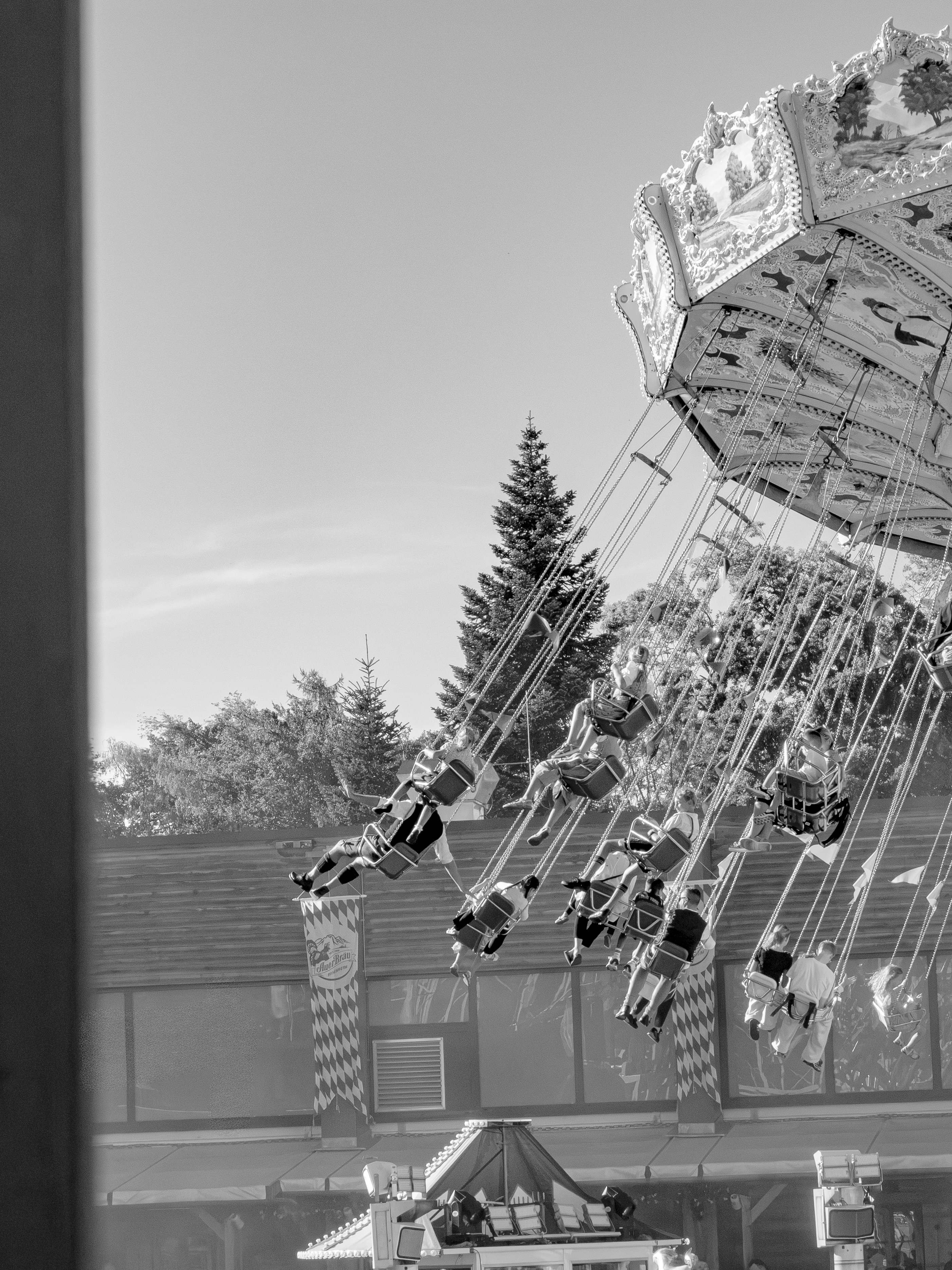 Motion-filled carousel riders suspended mid-air against a festive backdrop; grayscale tones emphasize contrast and motion in an outdoor fair scene.