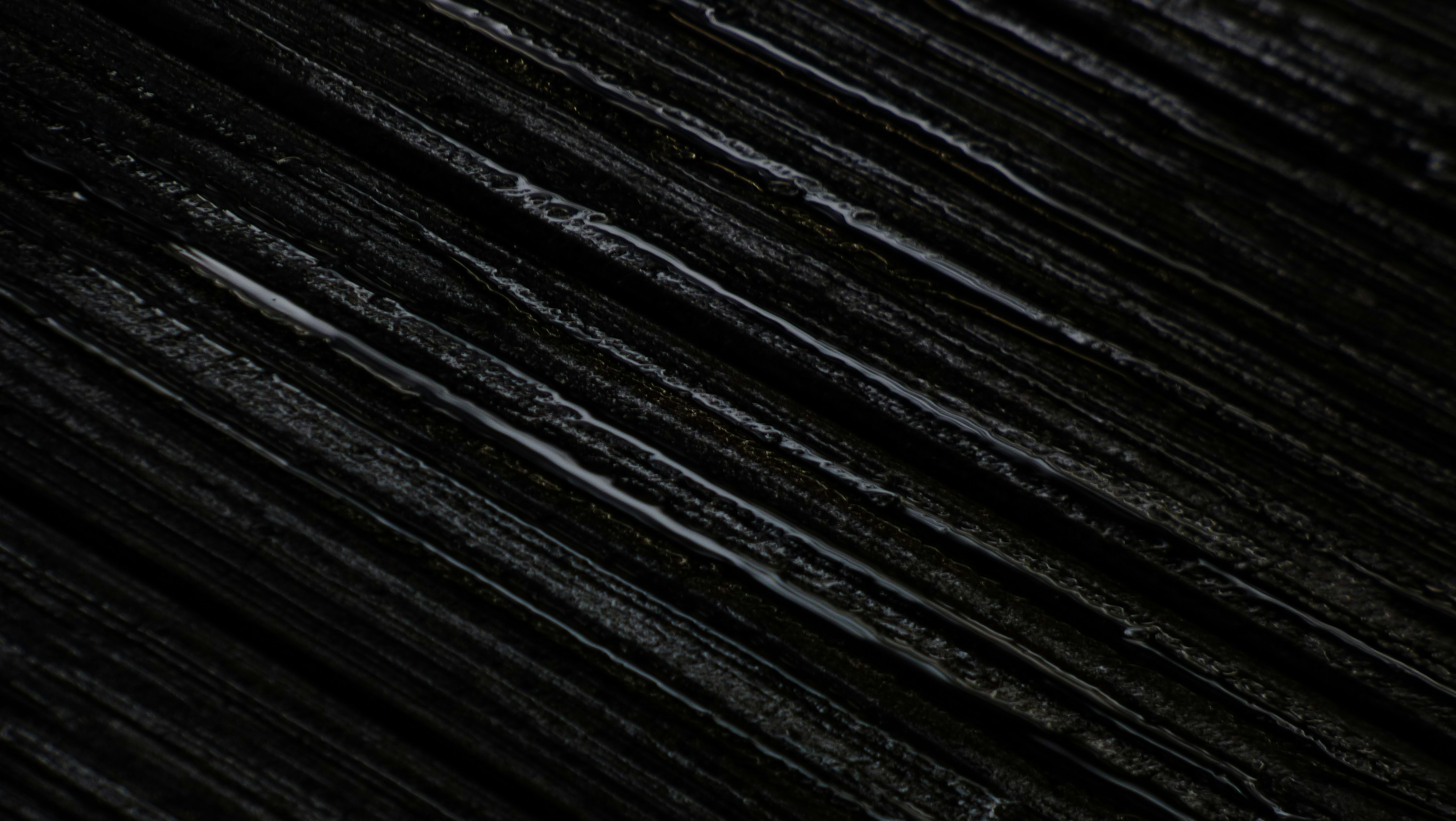 Dark, diagonal texture lines create a moody abstract surface with high contrast and subtle grain. The image focuses on the tactile pattern rather than any identifiable subject, conveying a minimalist, graphic feel.