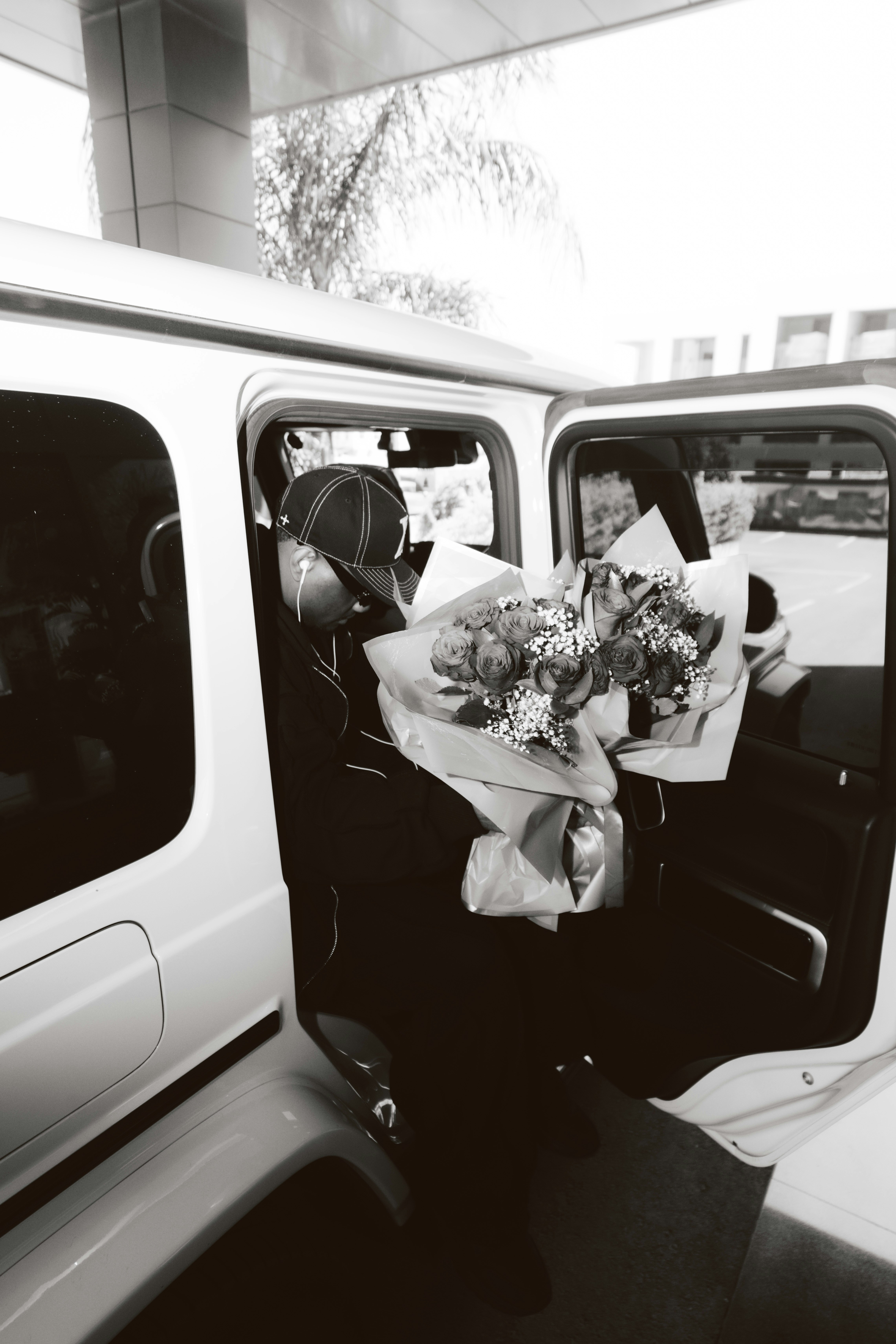 A person in a cap holding two large bouquets of roses inside a car