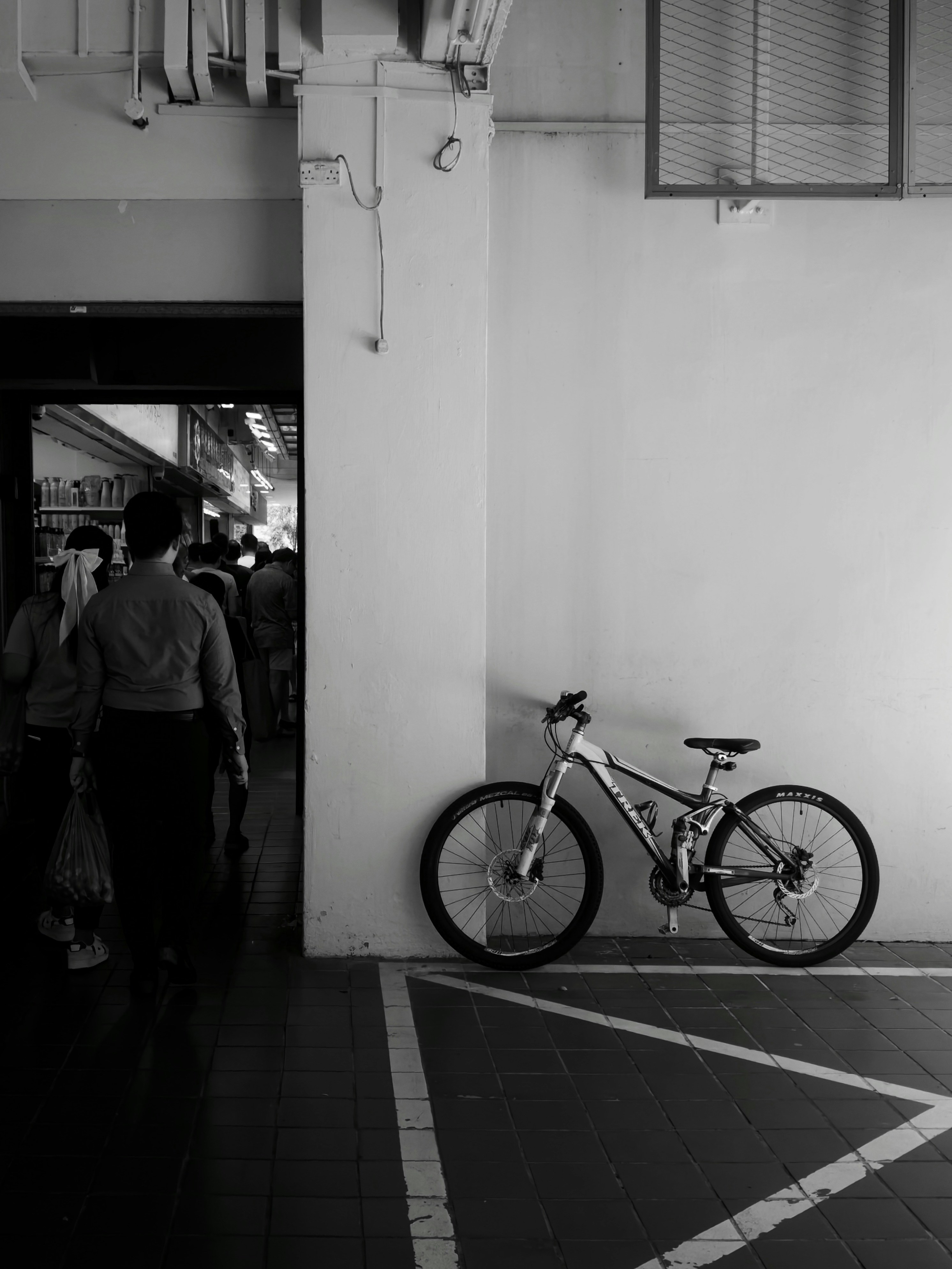 Bike leaned against a stark concrete wall, bustling doorway in the shadows