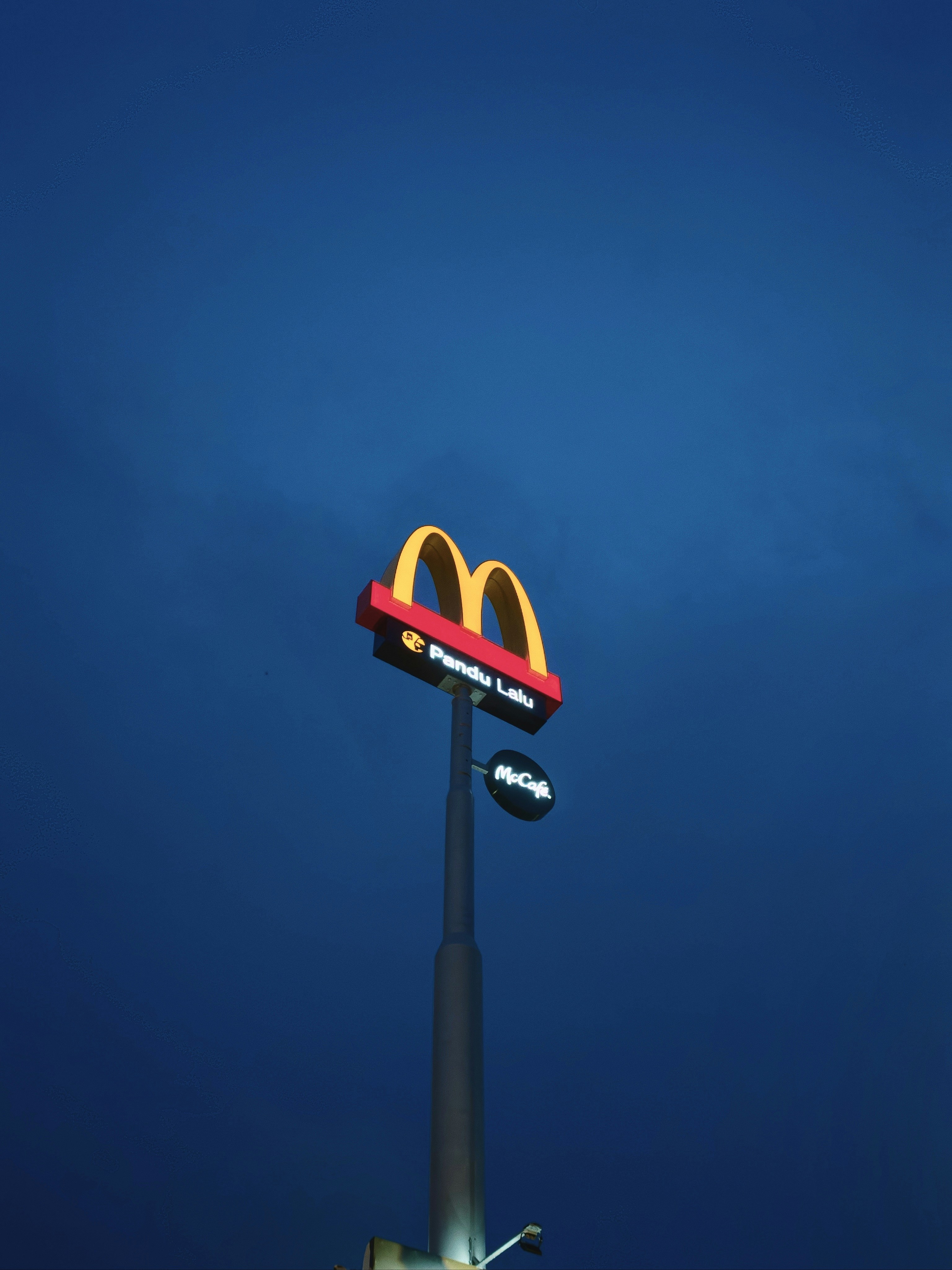 Tall pole with illuminated McDonald's arches and sign against a deep blue night sky; a secondary circular sign below dominates the lower portion of the frame.