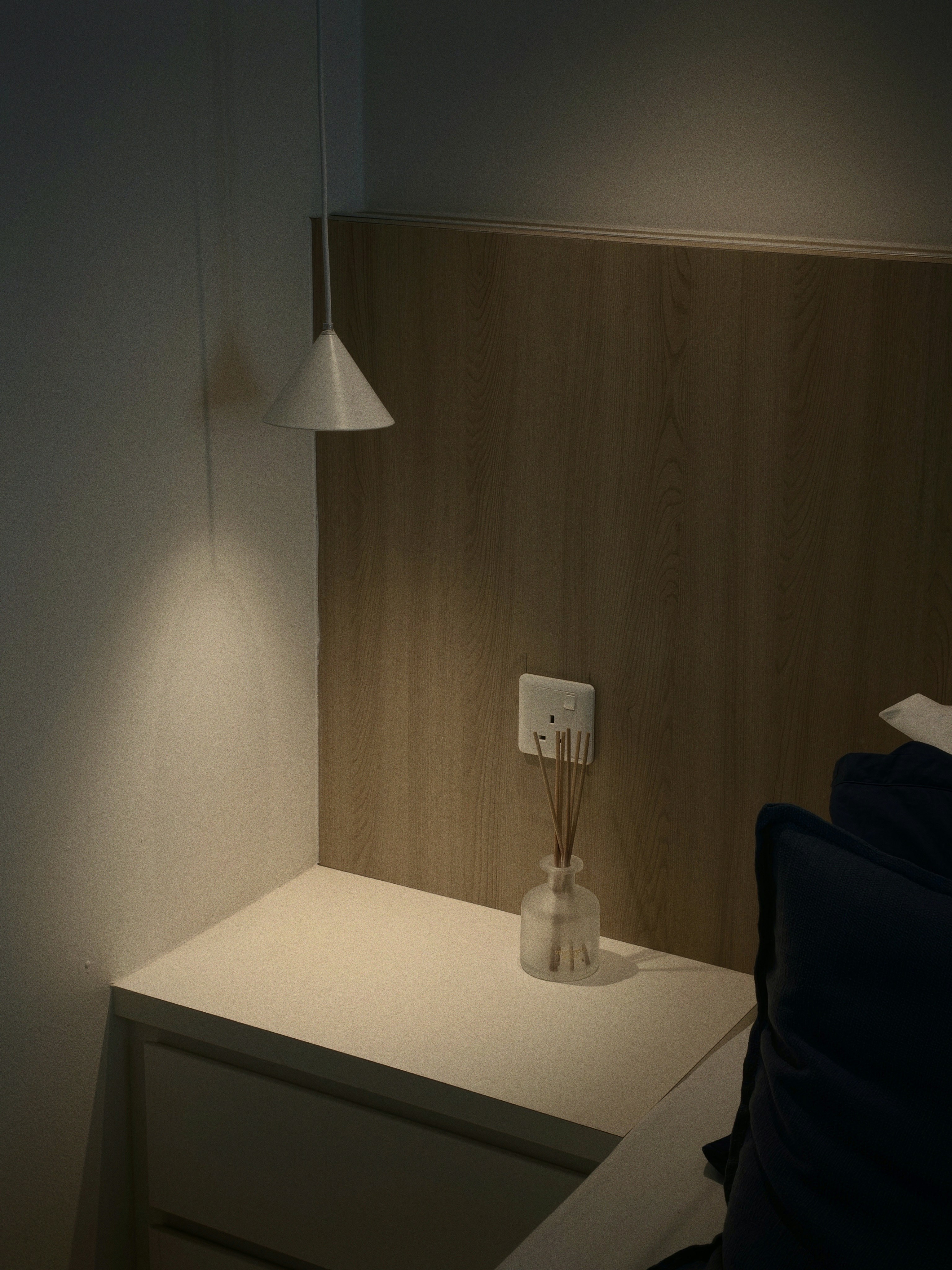 Softly lit corner with a desk, vase and reed diffuser against a wooden backdrop in a muted, cozy interior.