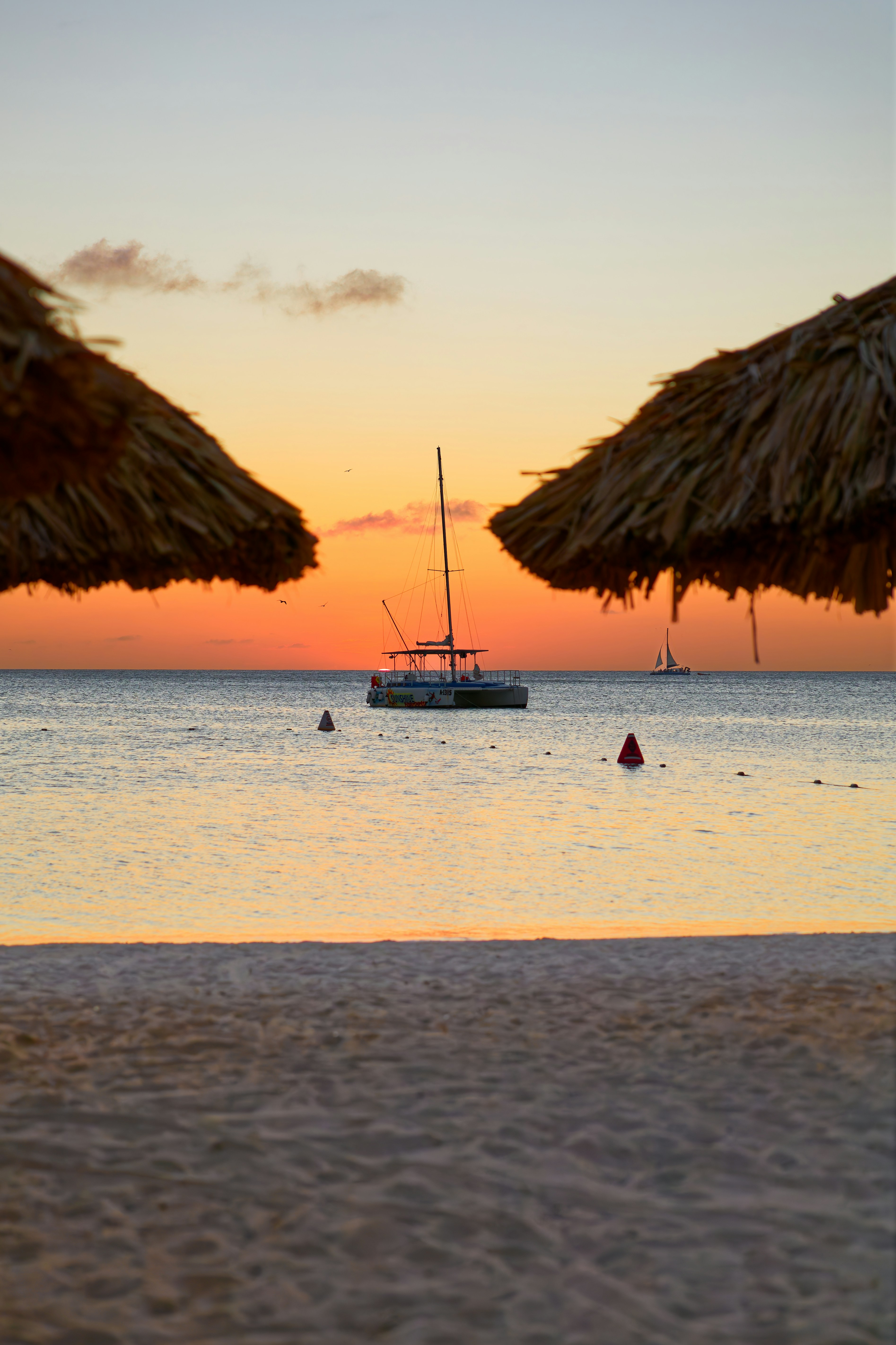 Sailboat at Sunset Between Palm-thatched Silhouettes