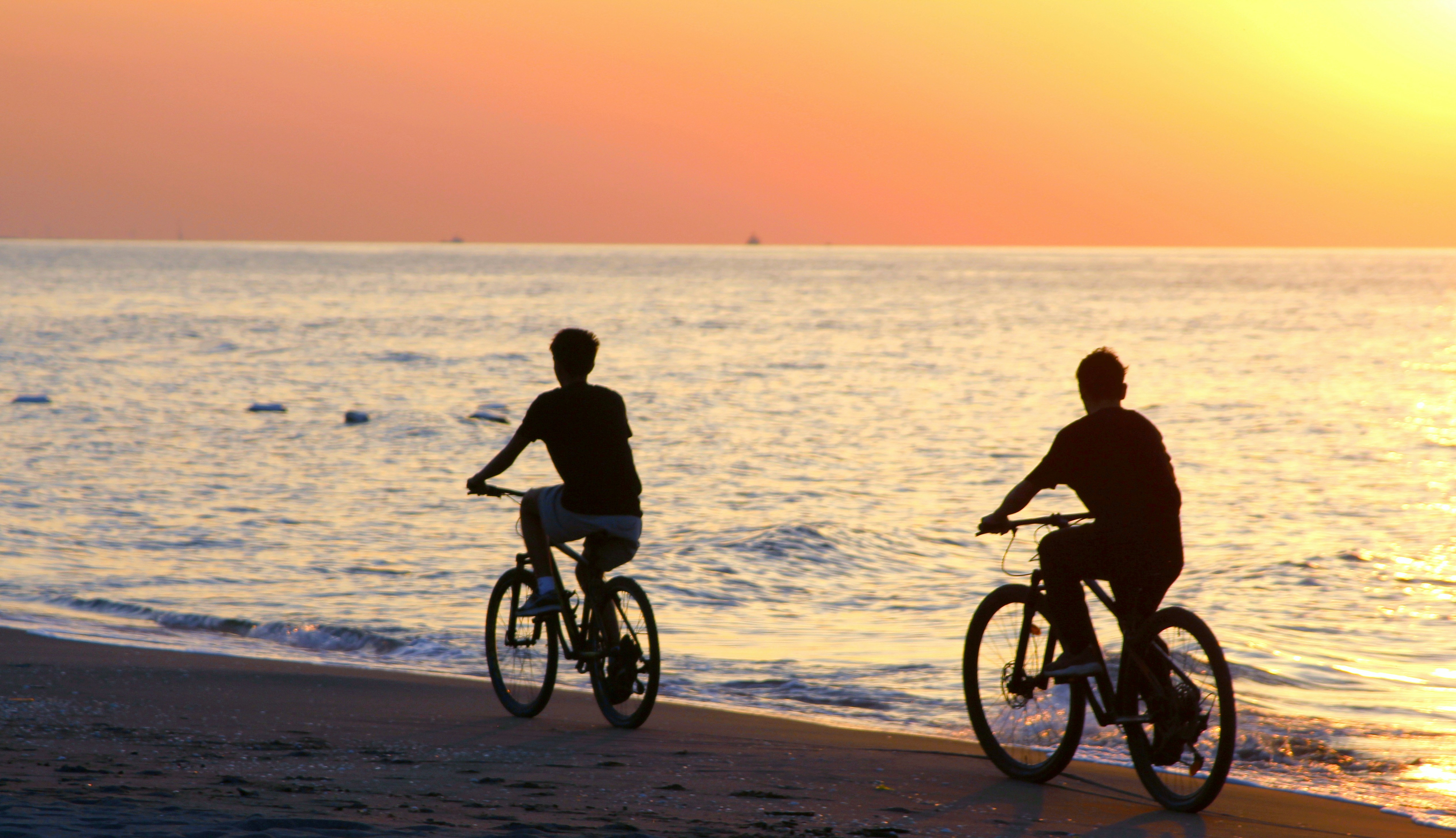 Two silhouettes ride the shoreline at sunset, horizons painted in warm hues