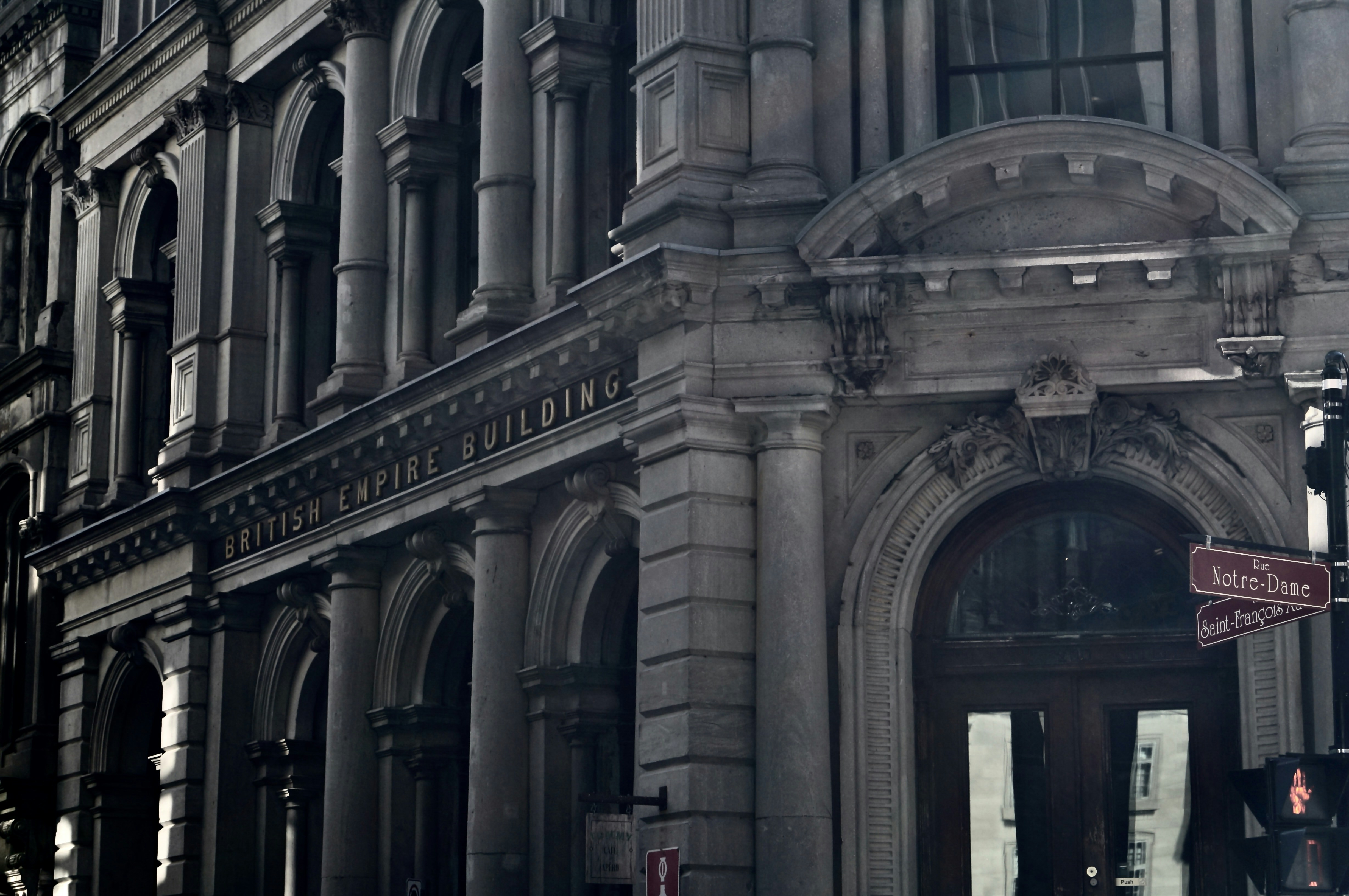 Corner of a historic stone building with arches and ornate details; the scene emphasizes architectural texture and signage against a muted urban backdrop.