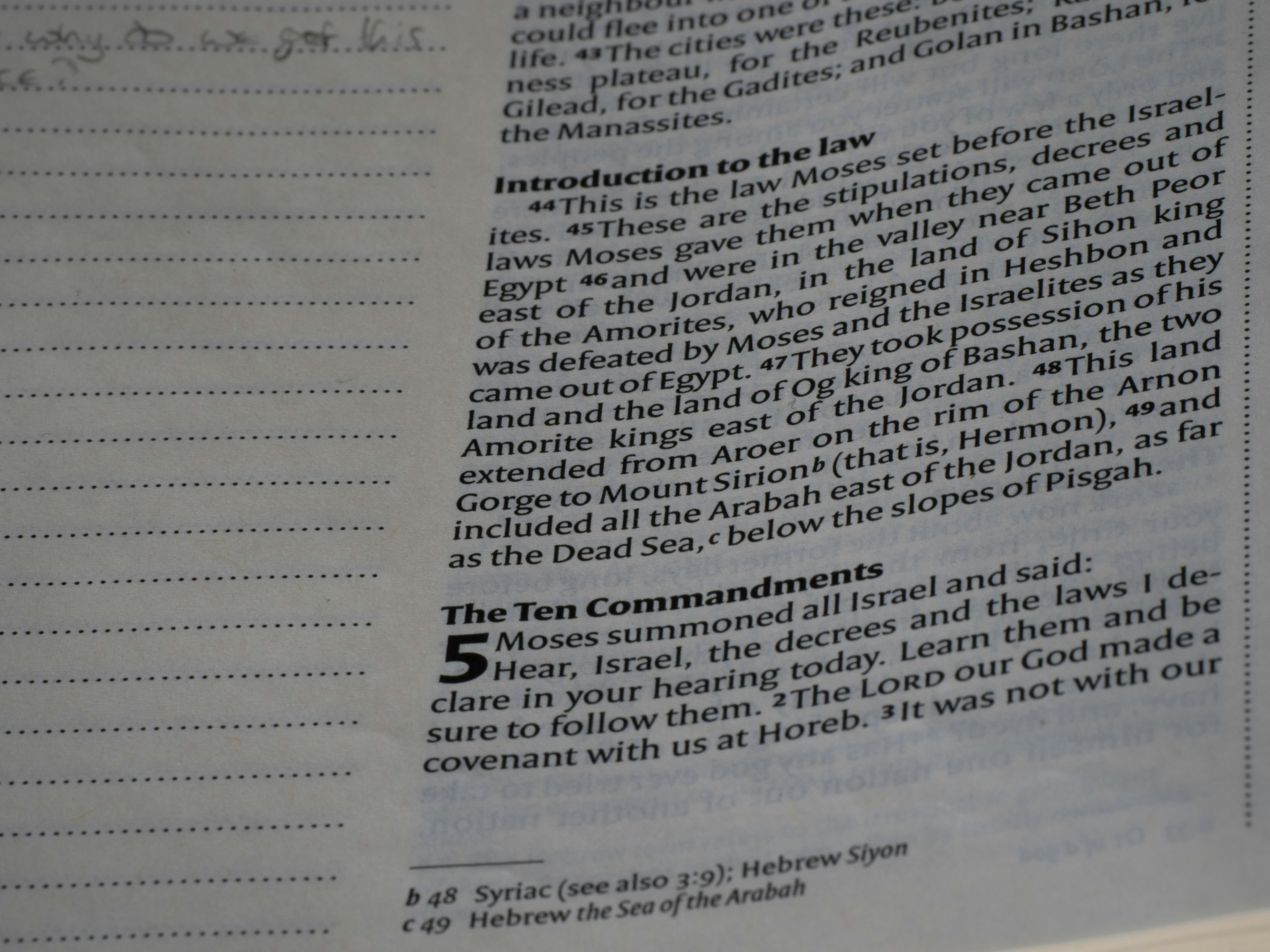 A page from a printed text shows the Ten Commandments with surrounding commentary in a close-up, softly lit and slightly angled reading scene. This is a printed illustration of a religious text in a book or pamphlet.