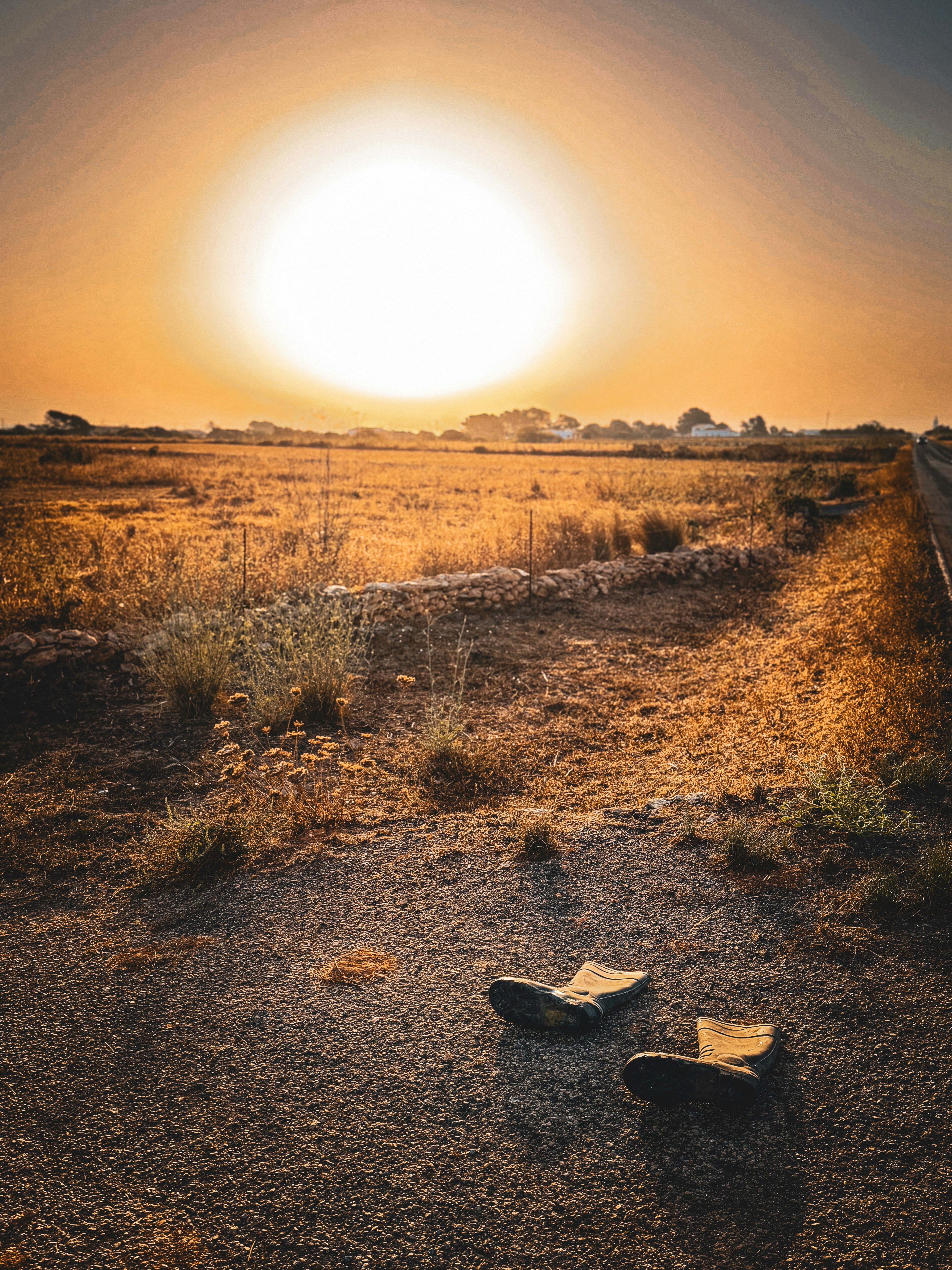 Two rubber boots on a gravel roadside under a low golden sun