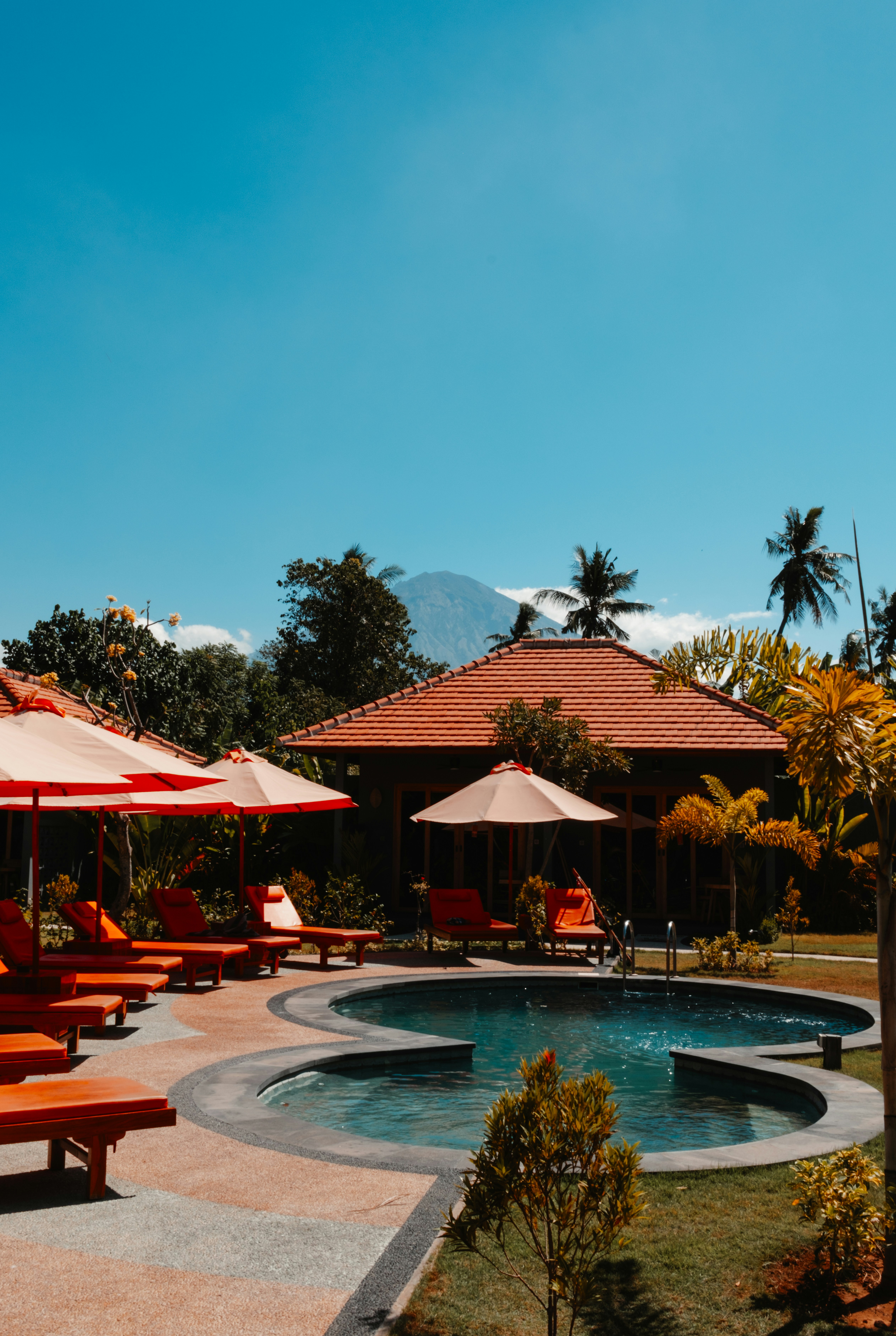 Tropical Poolside Retreat with Red-Orange Loungers and Thatched Roof Cabin