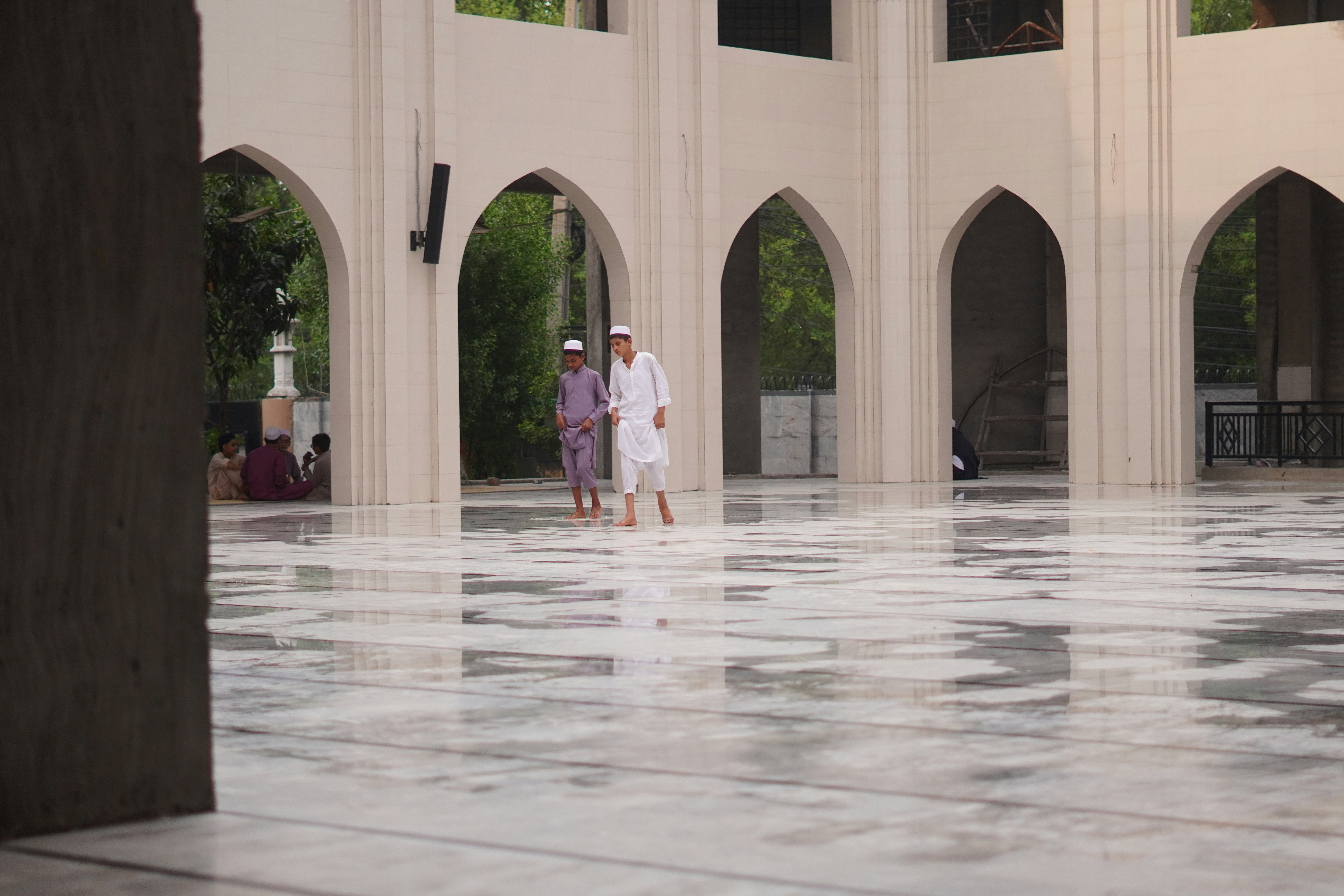 Two figures in white and purple walk across a marble courtyard framed by archways
