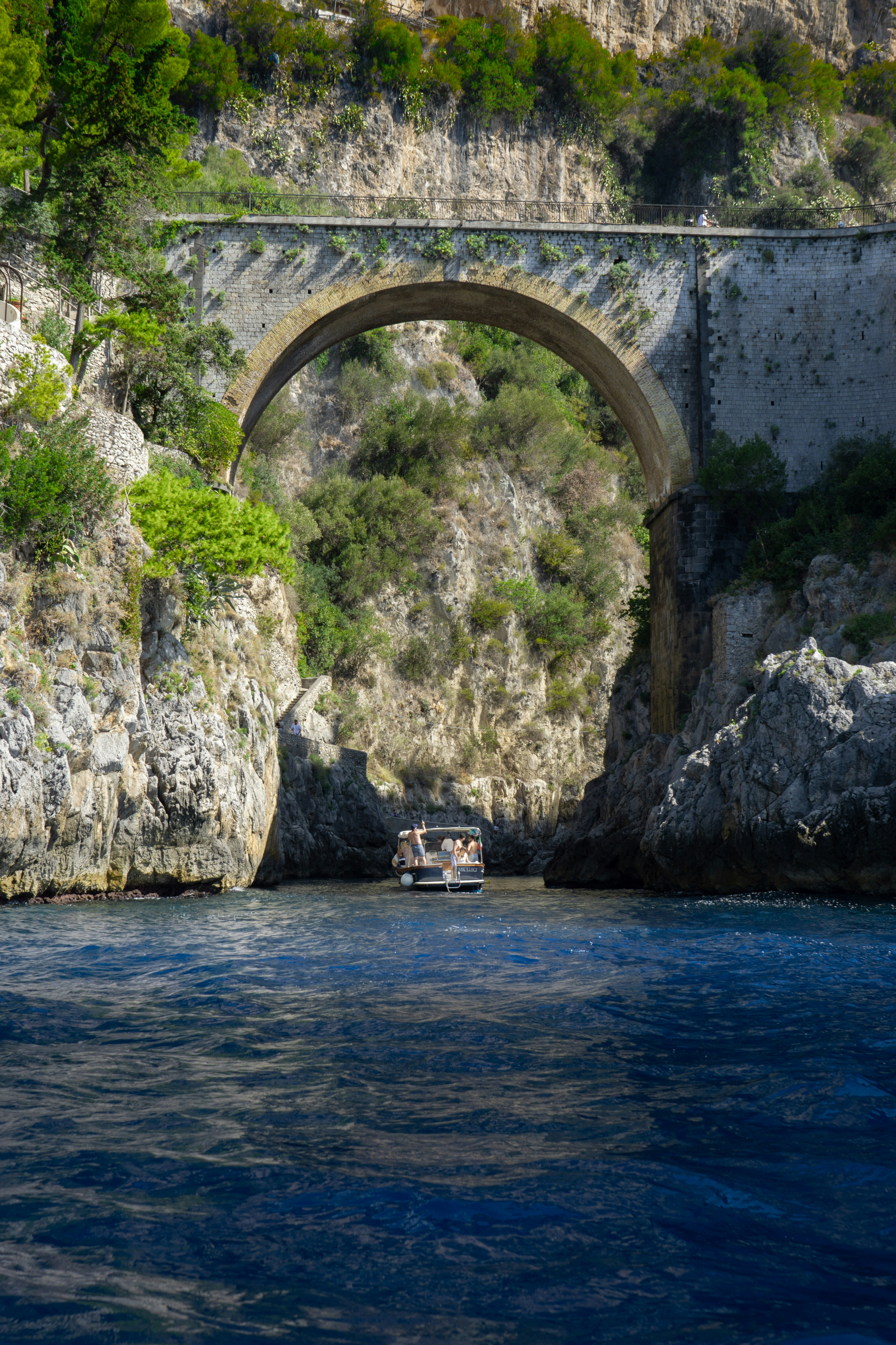 A small boat carrying people through a narrow rocky gorge under a stone bridge