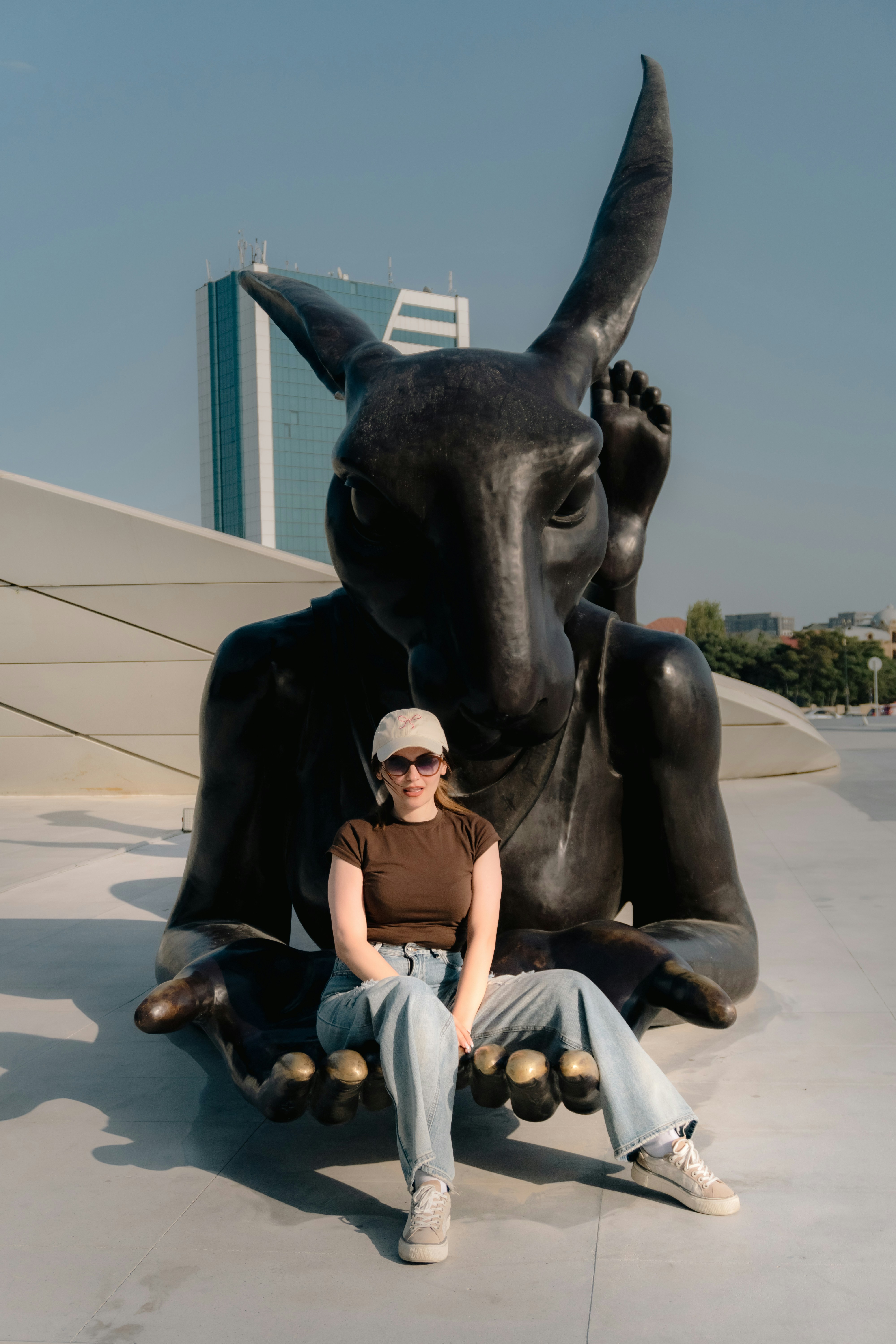 Girl in front of a colossal horned sculpture at a sunlit plaza