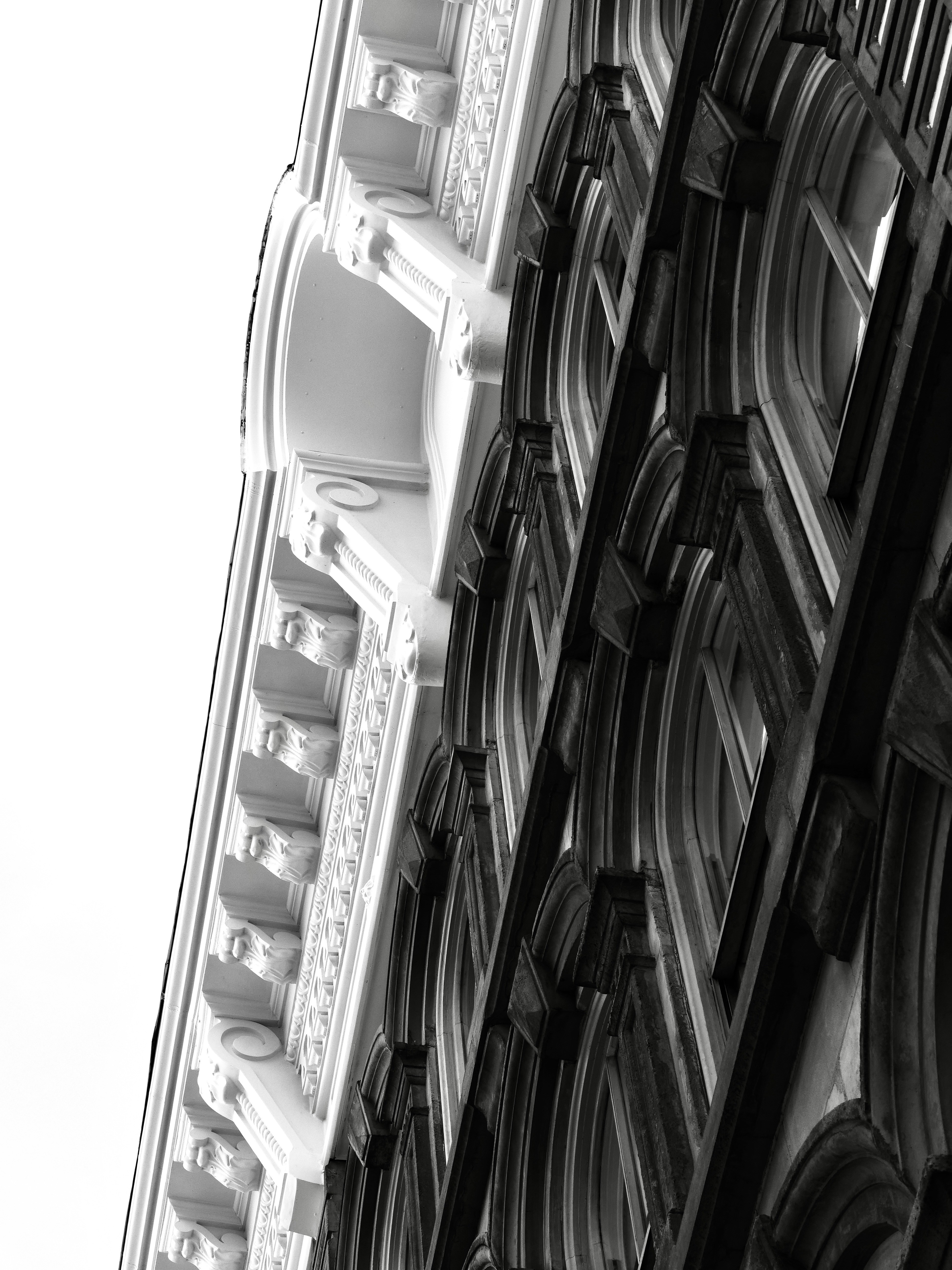 Monochrome architectural façade with ornate cornices and arched windows, captured at an angle to emphasize texture and depth.