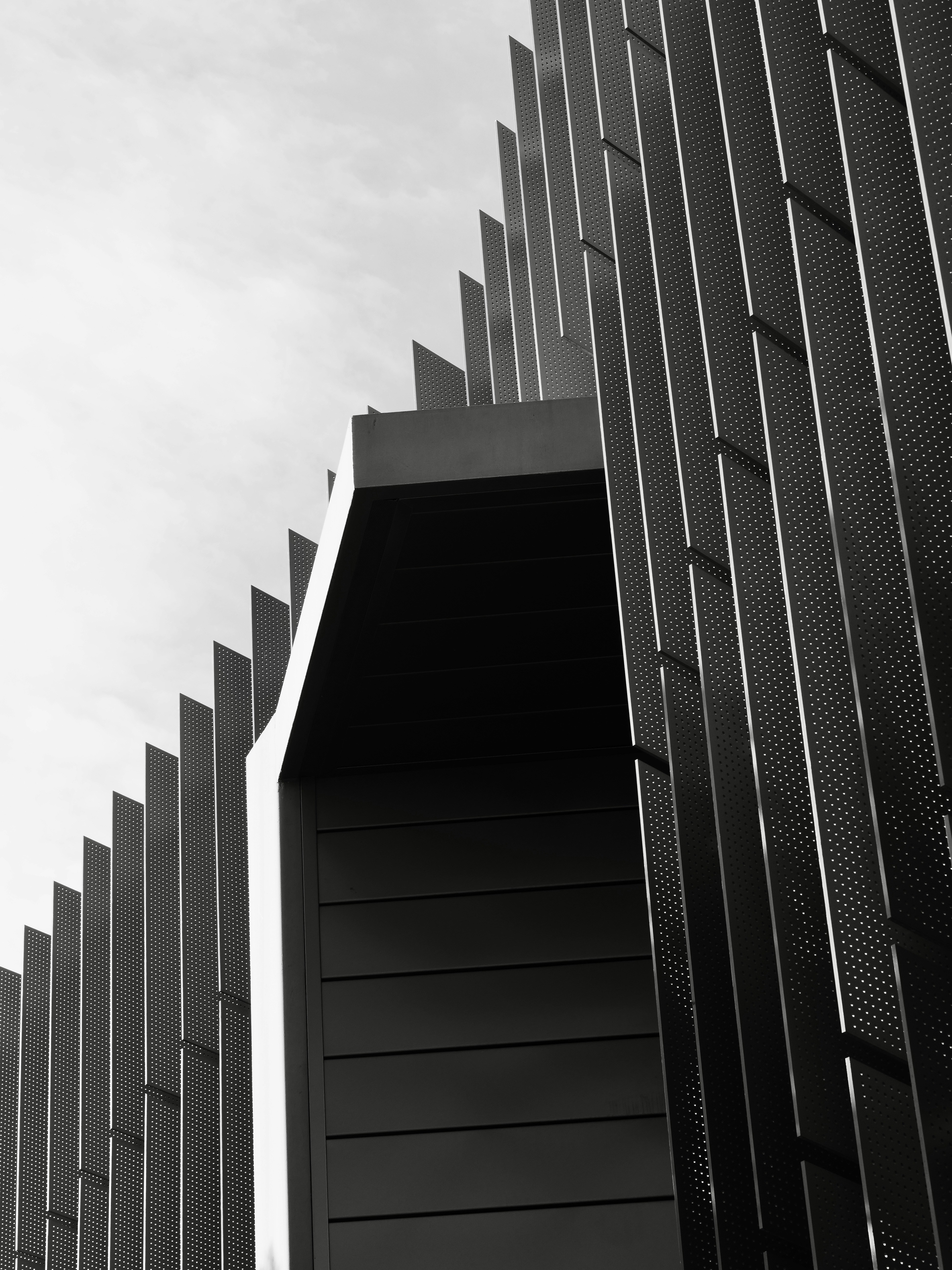Monochrome architectural detail of a modern building with stepped perforated panels and a dark recessed entry, emphasizing geometric repetition and contrast.