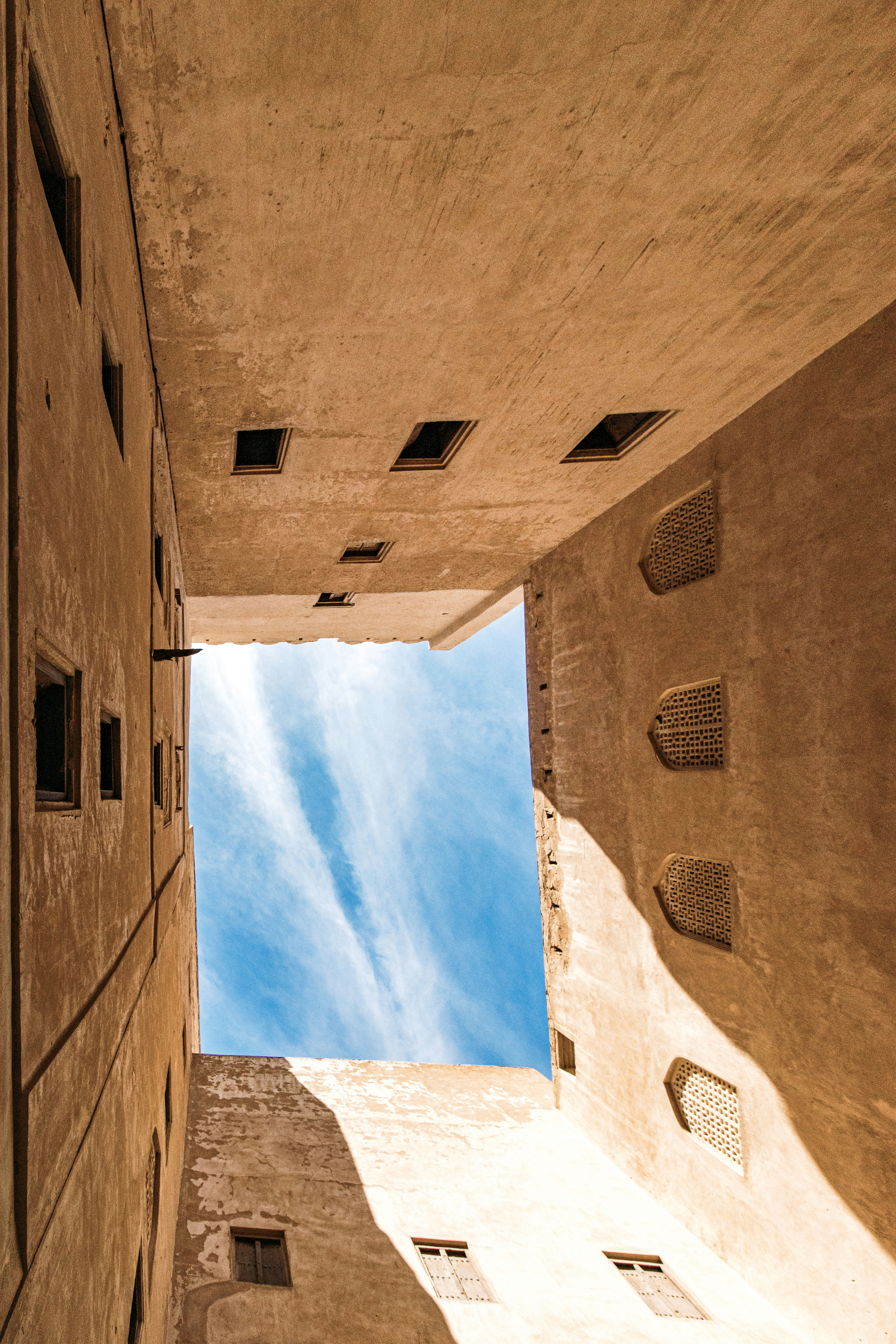 Low angle view of beige stone walls with small windows framing a blue sky