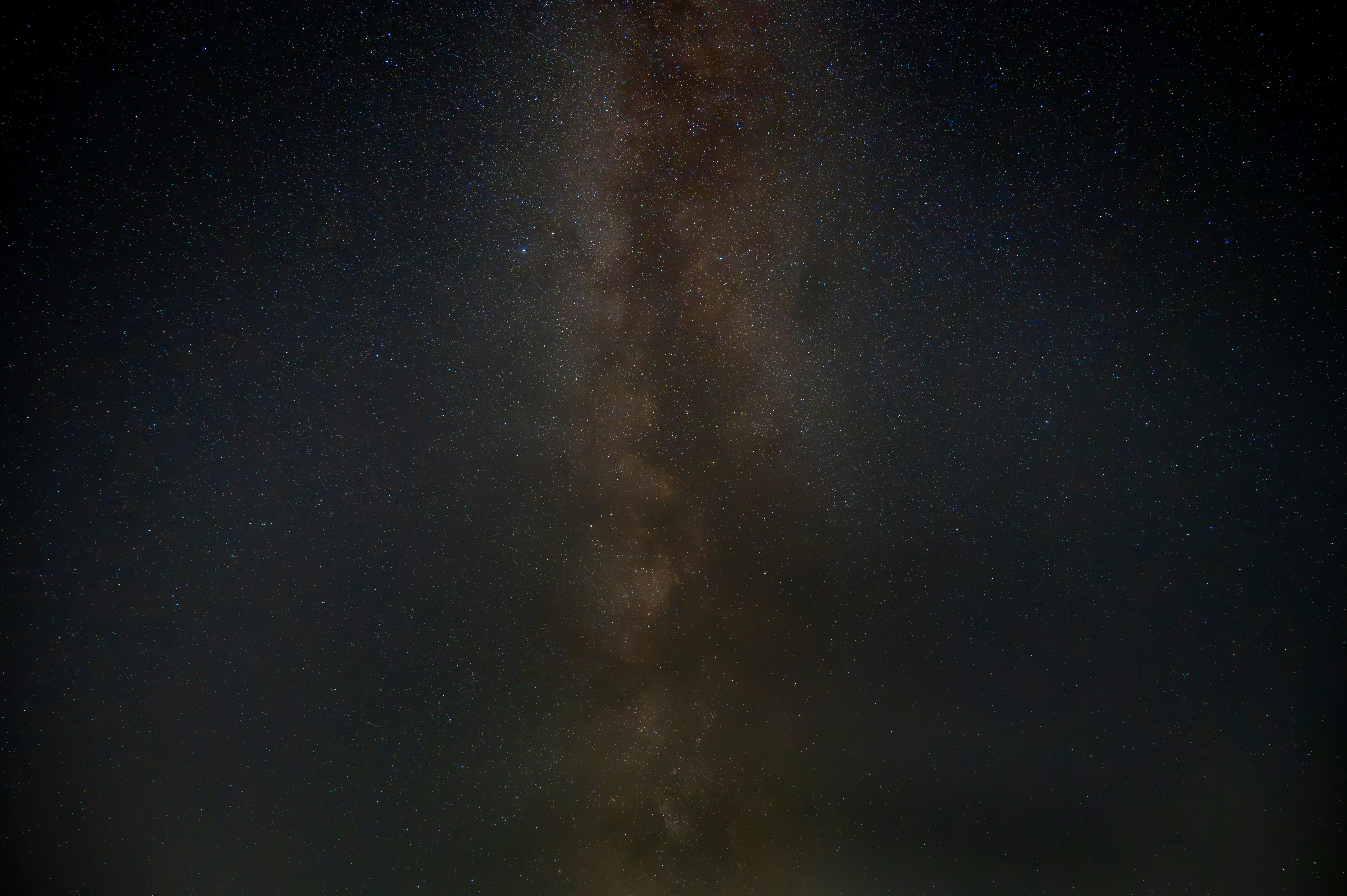 Star-filled night sky with prominent Milky Way core rising above a dark horizon, captured in a wide celestial panorama.