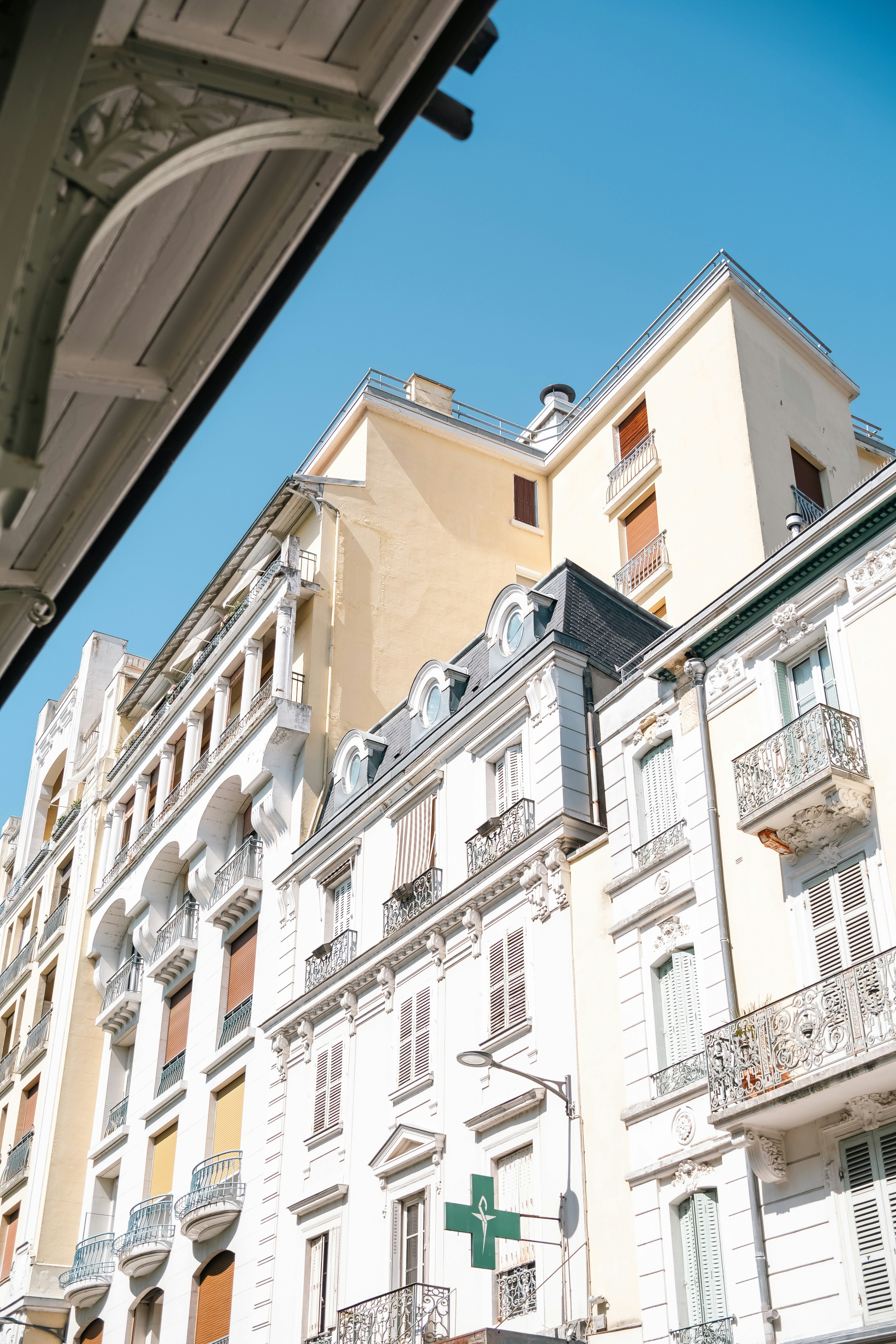 White and pastel city buildings with ornate balconies rise toward a bright blue sky.