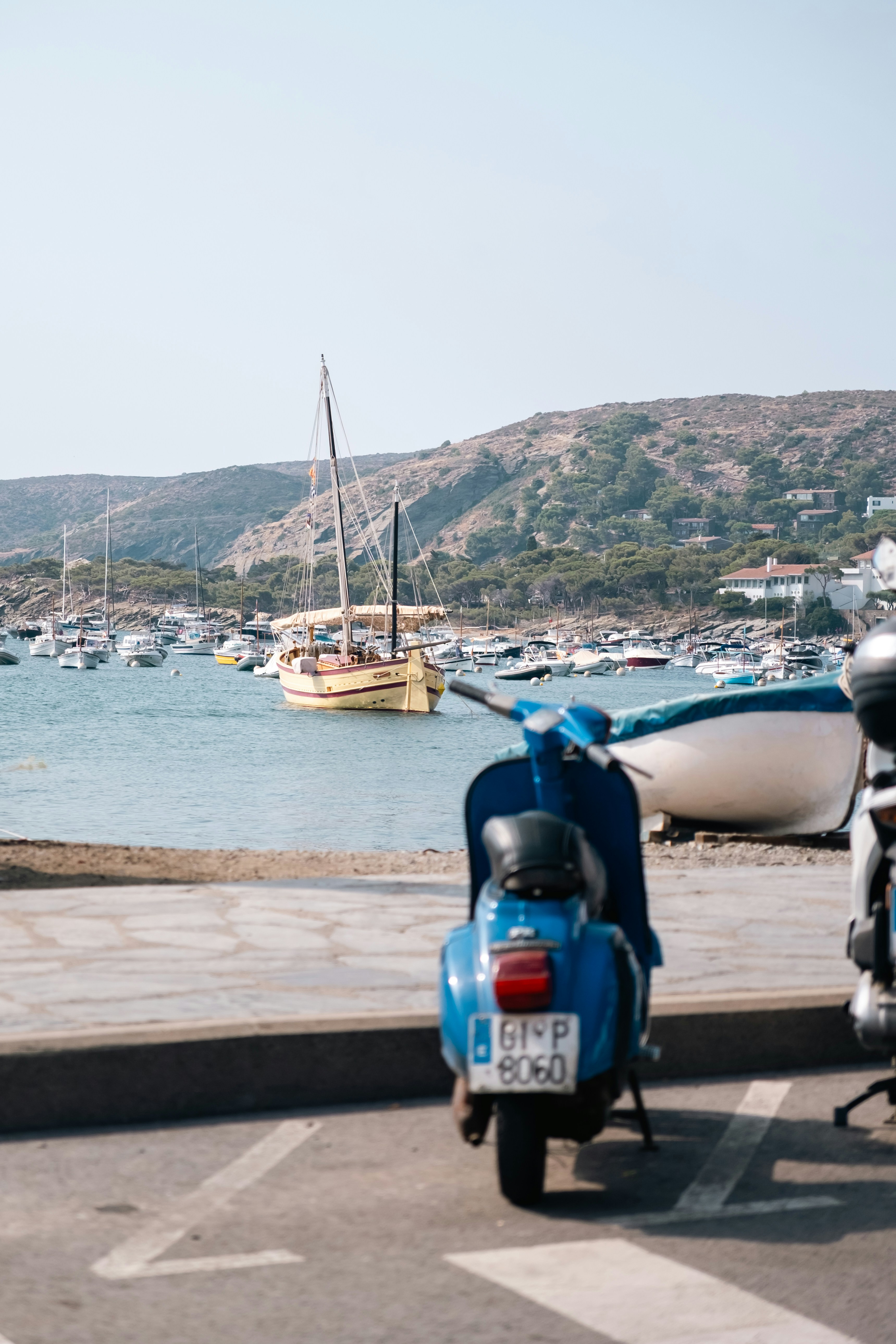 Blue Scooter by the Quiet Marina: Boats and Hillside Charm