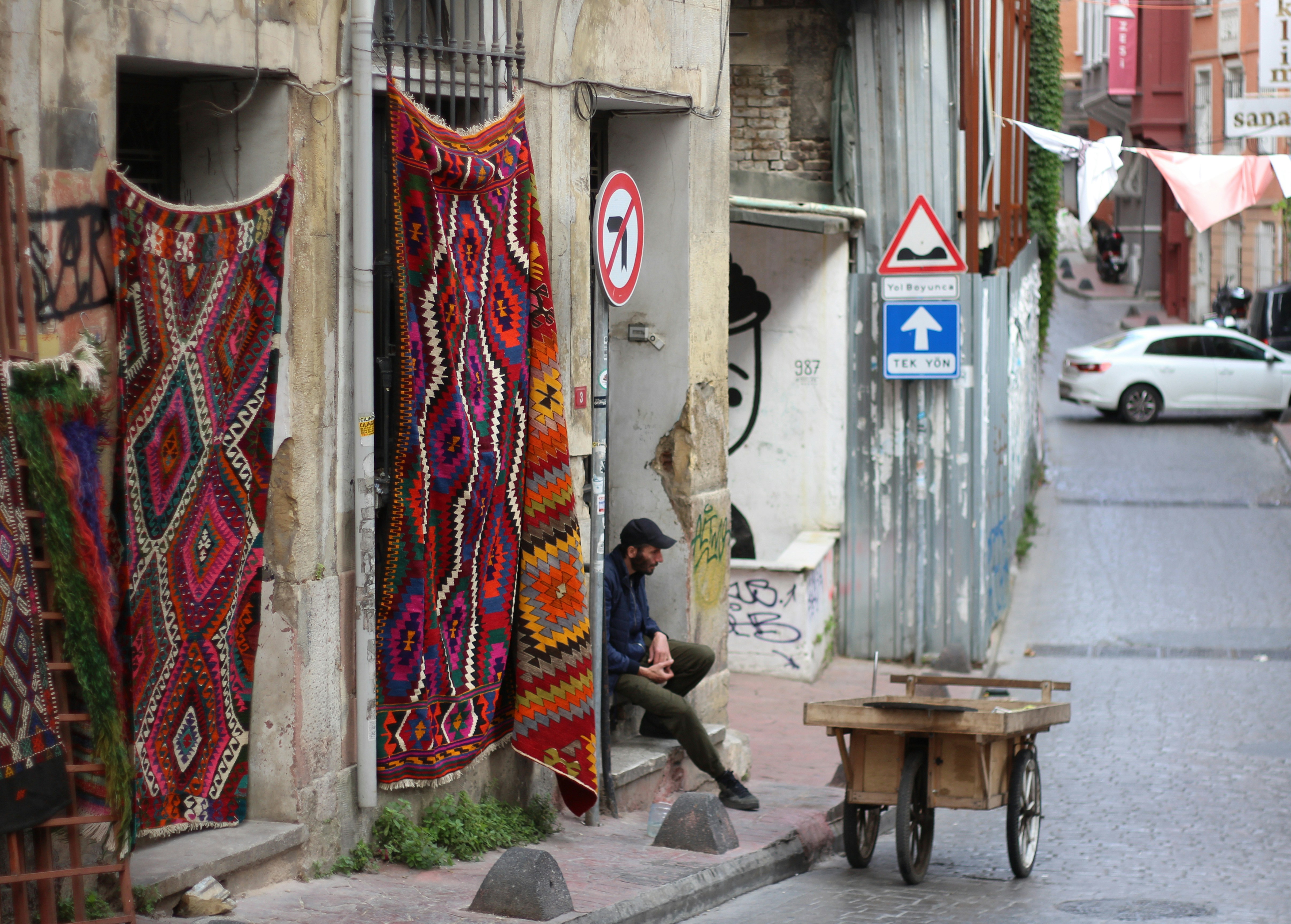 Street Carpet Gallery: A Quiet Corner with Aged Facades and a Seated Onlooker