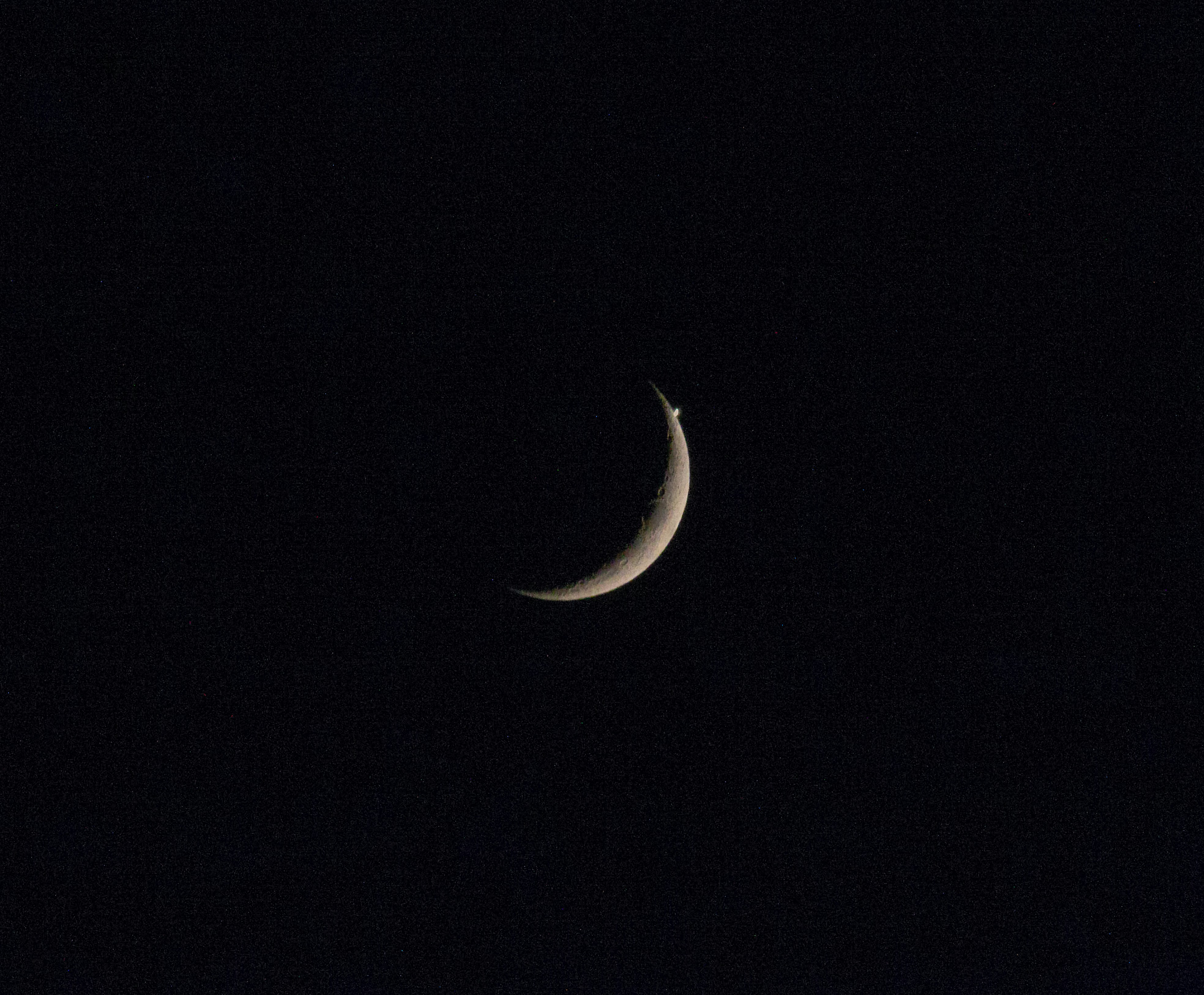 A thin crescent moon glowing against a vast dark night sky