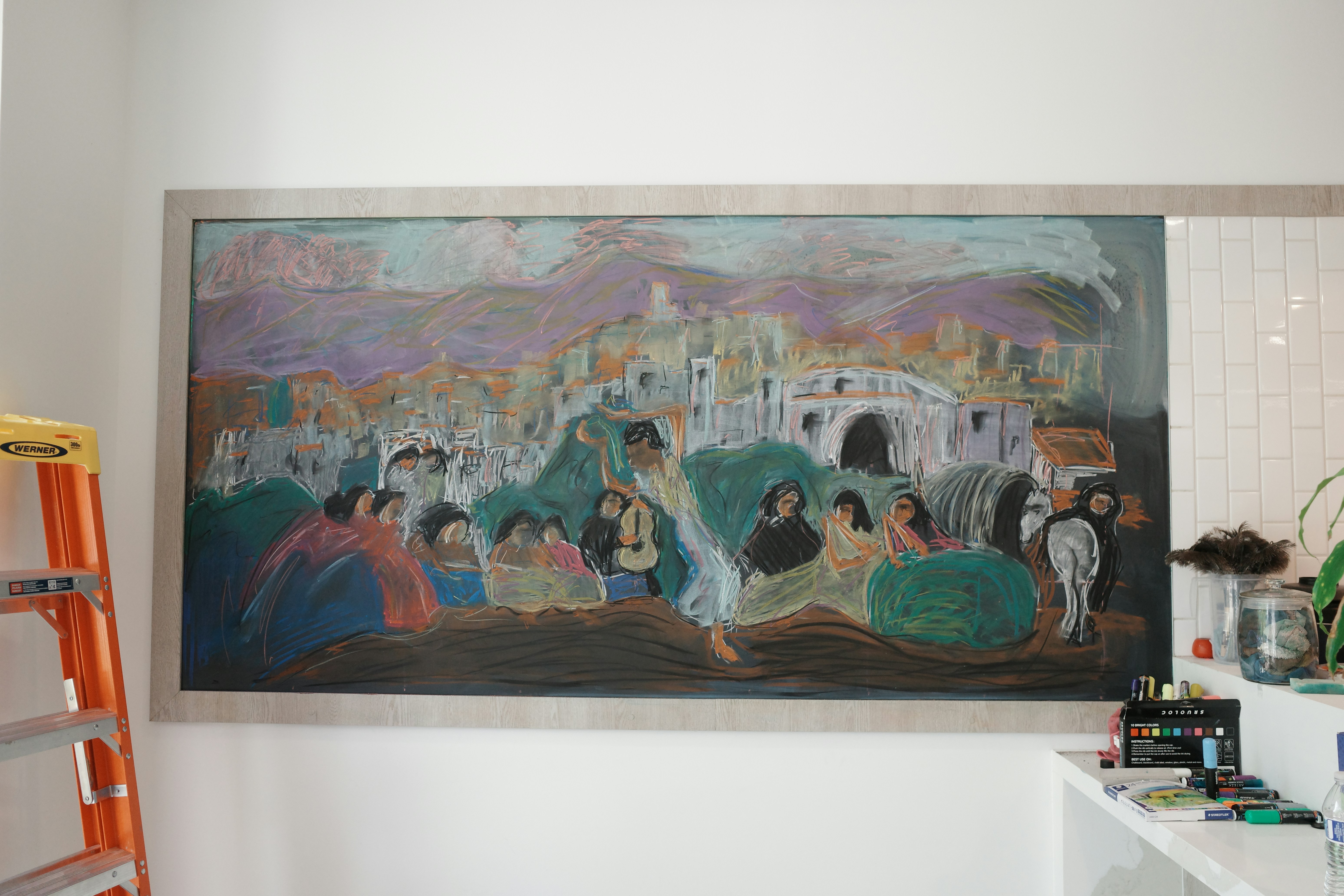 Colorful mural-style painting of boats and people mounted on a white wall in a room; a small shelf with items sits to the right and an orange ladder leans against the left wall.