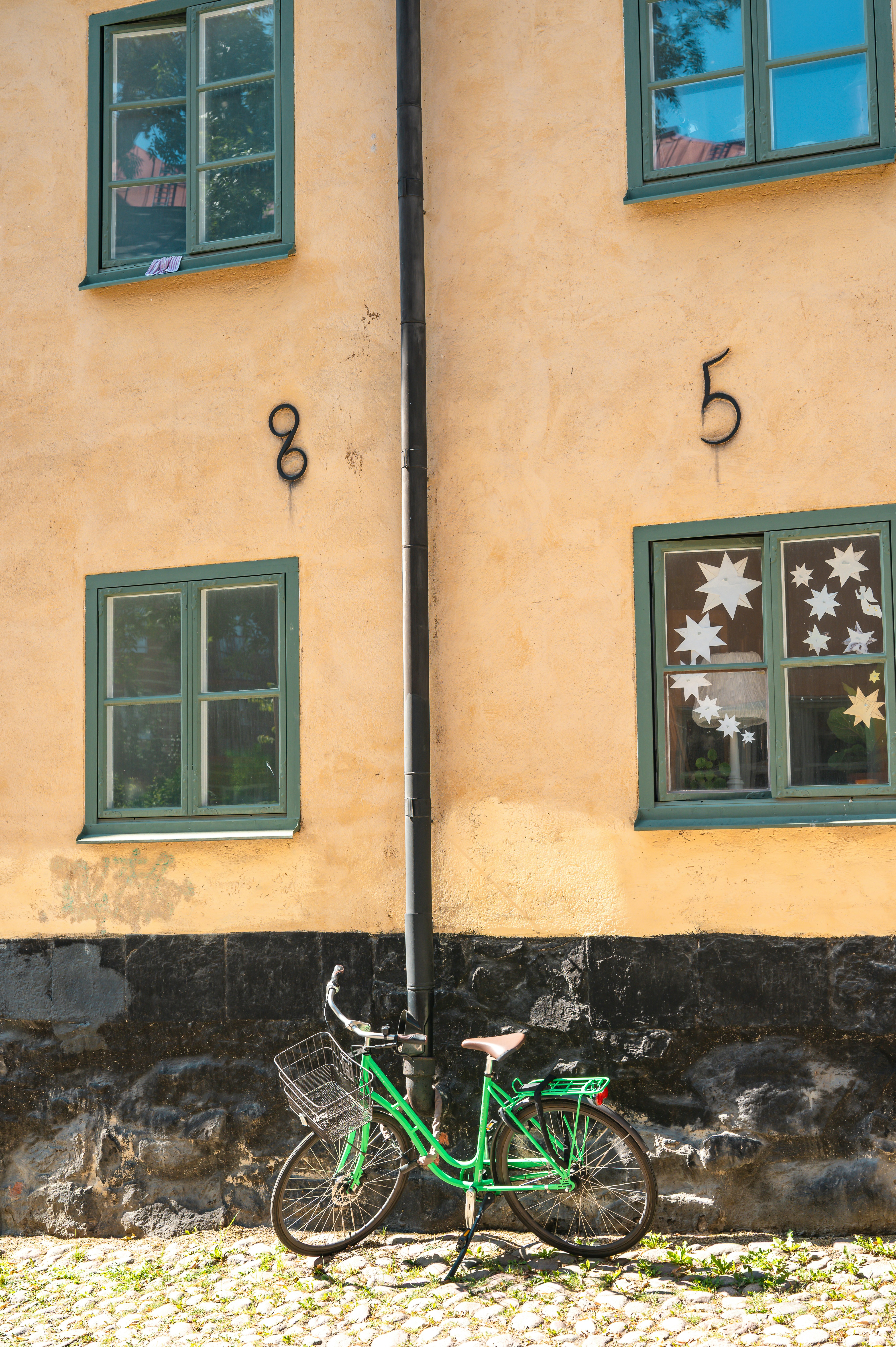 Green bicycle at the base of a sunlit yellow building with star-decorated window