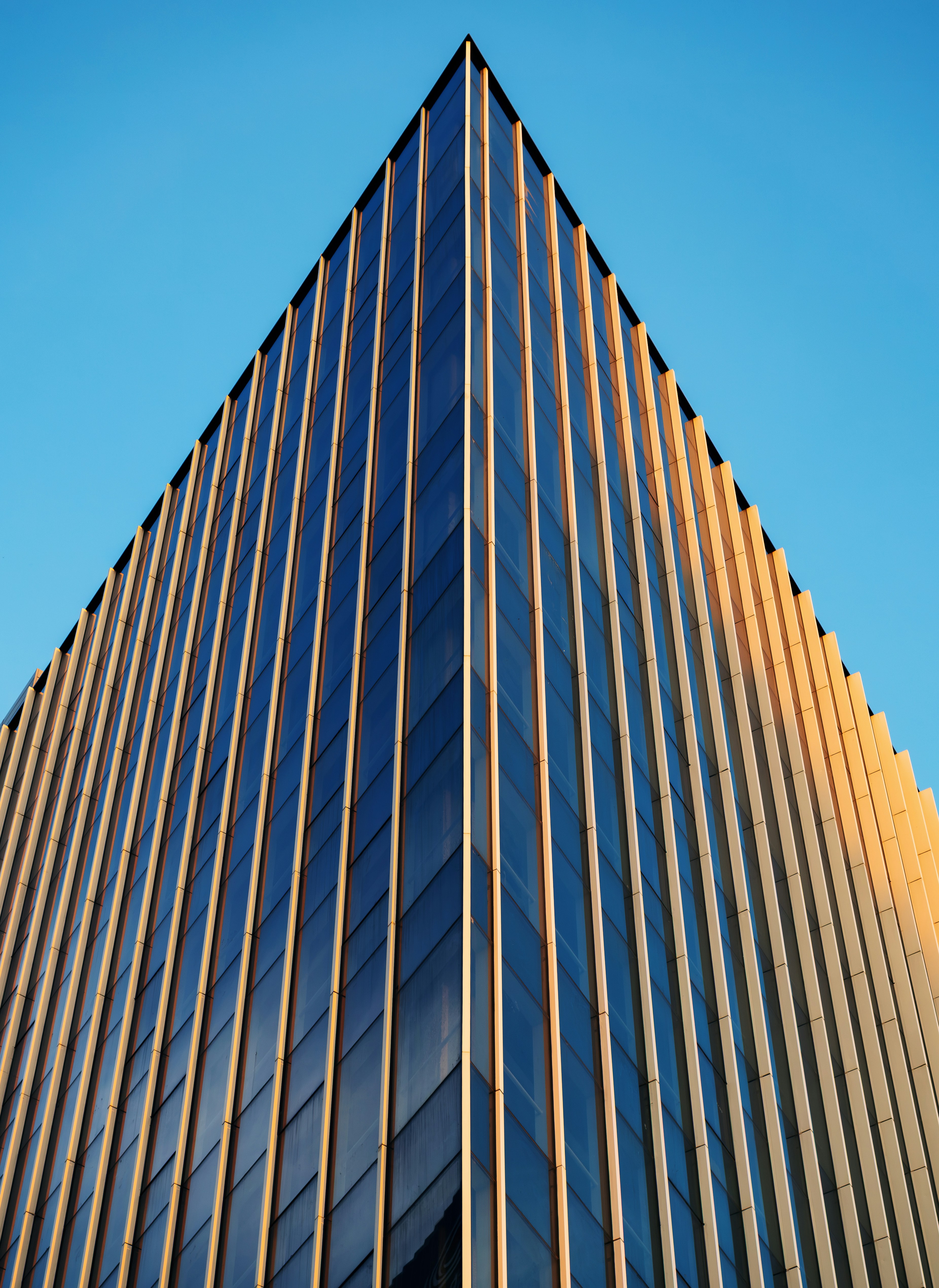 Sleek glass-and-metal skyscraper edge forming a dramatic V, captured from a low angle against a clear blue sky.
