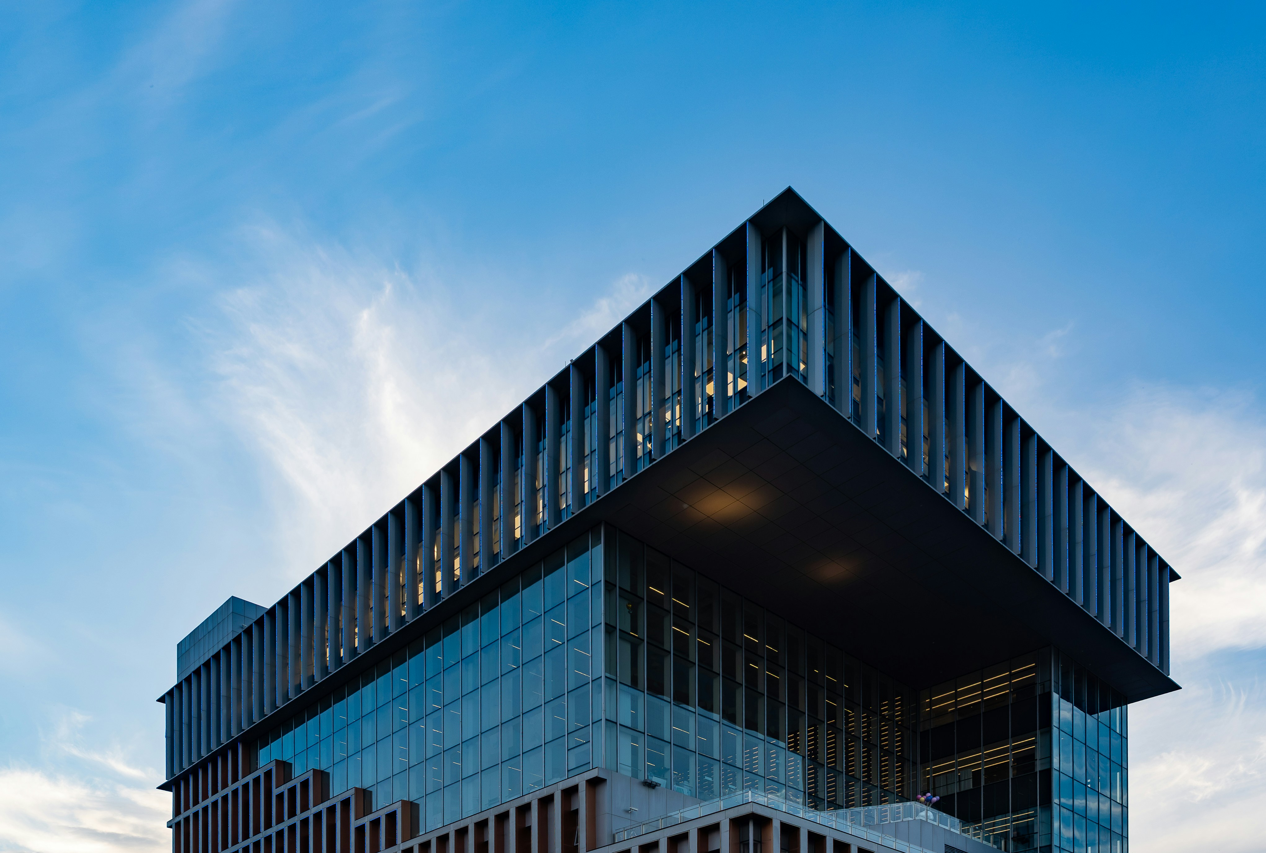 Angular modern building corner rising against a clear blue sky with reflective glass panels and ribbed facade.</p>