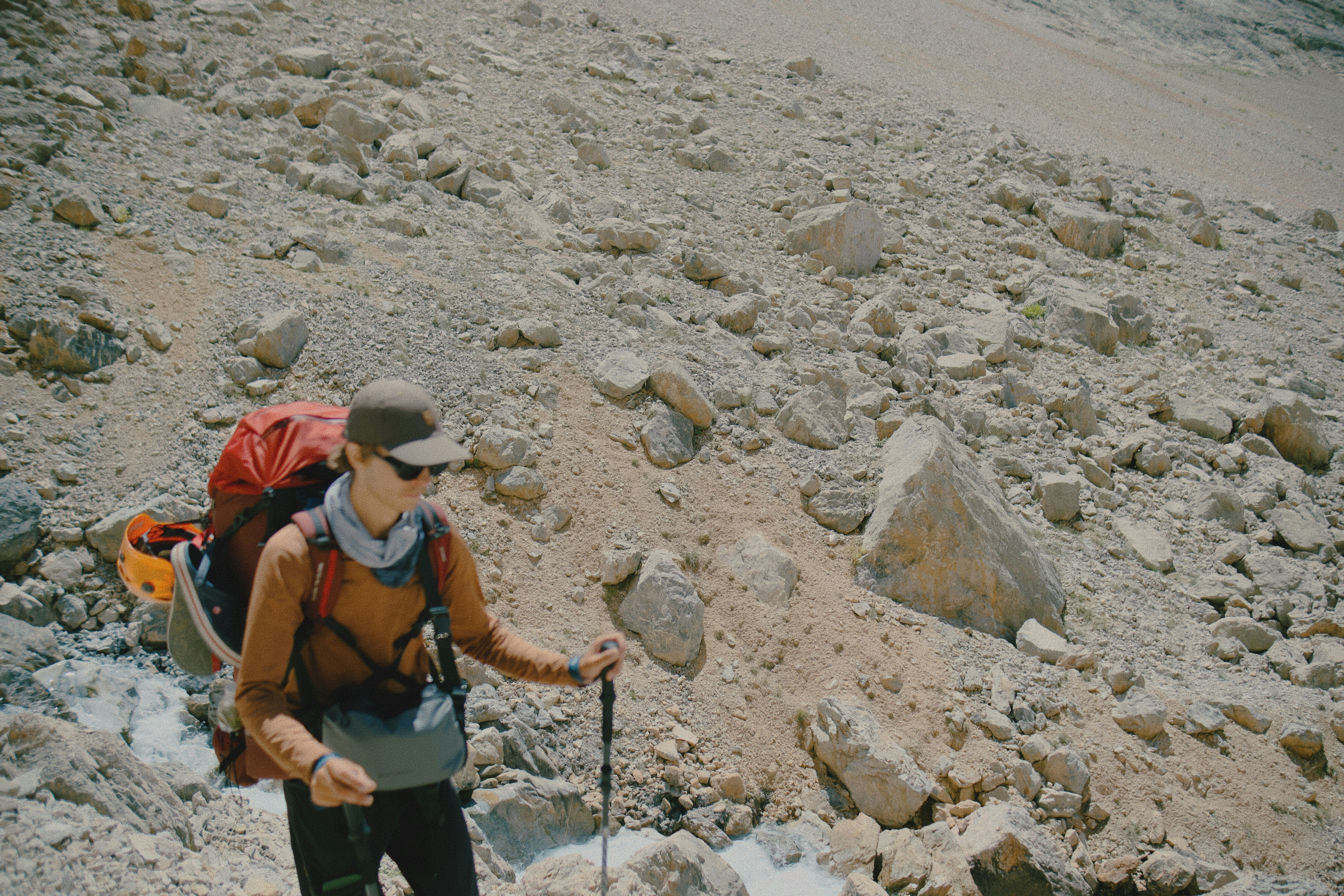 Red‑backpack Trek: a climber navigates rocky terrain under a pale sky