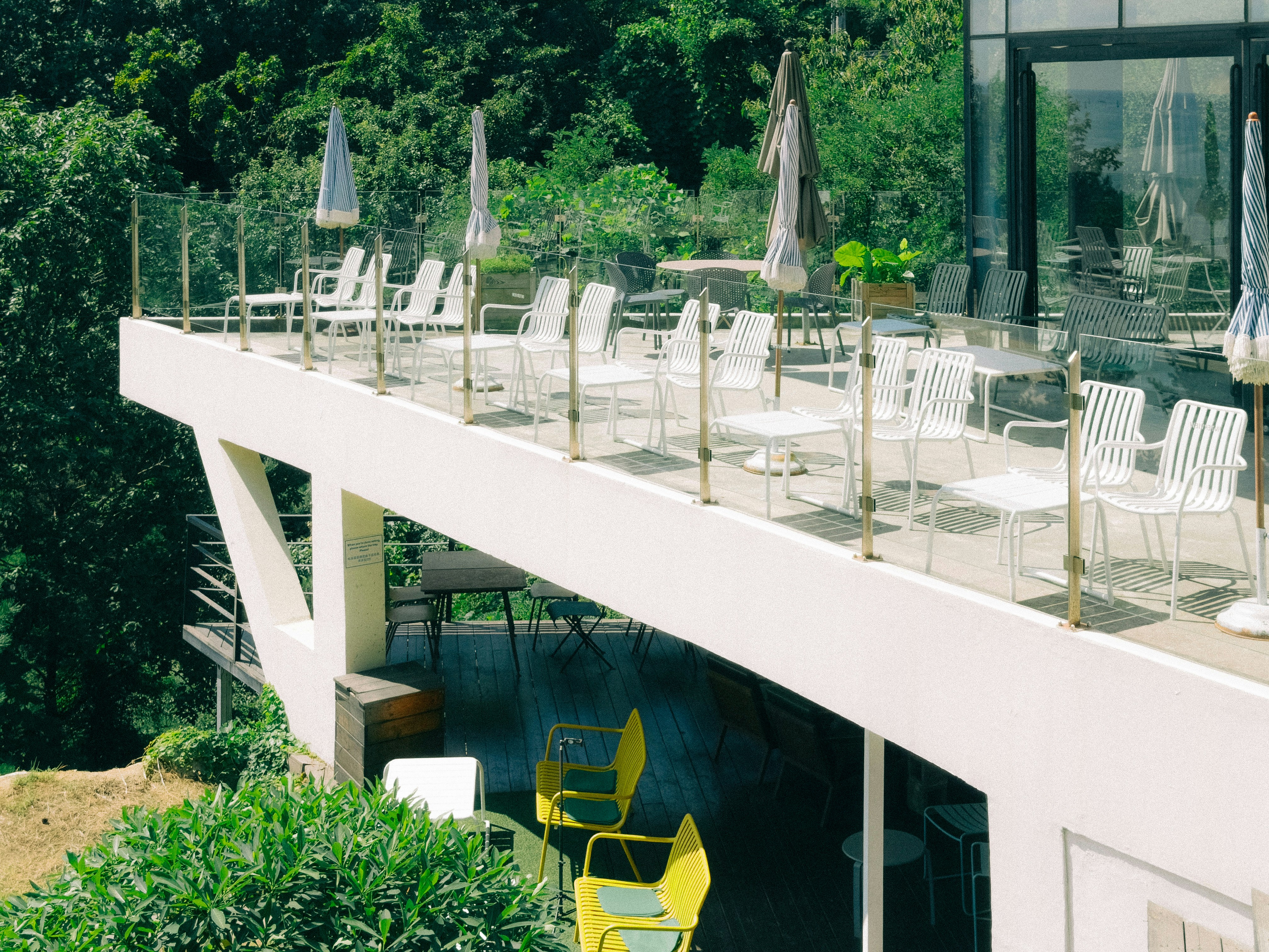 Balcony overhang: sunlit terrace with white chairs and glass railing