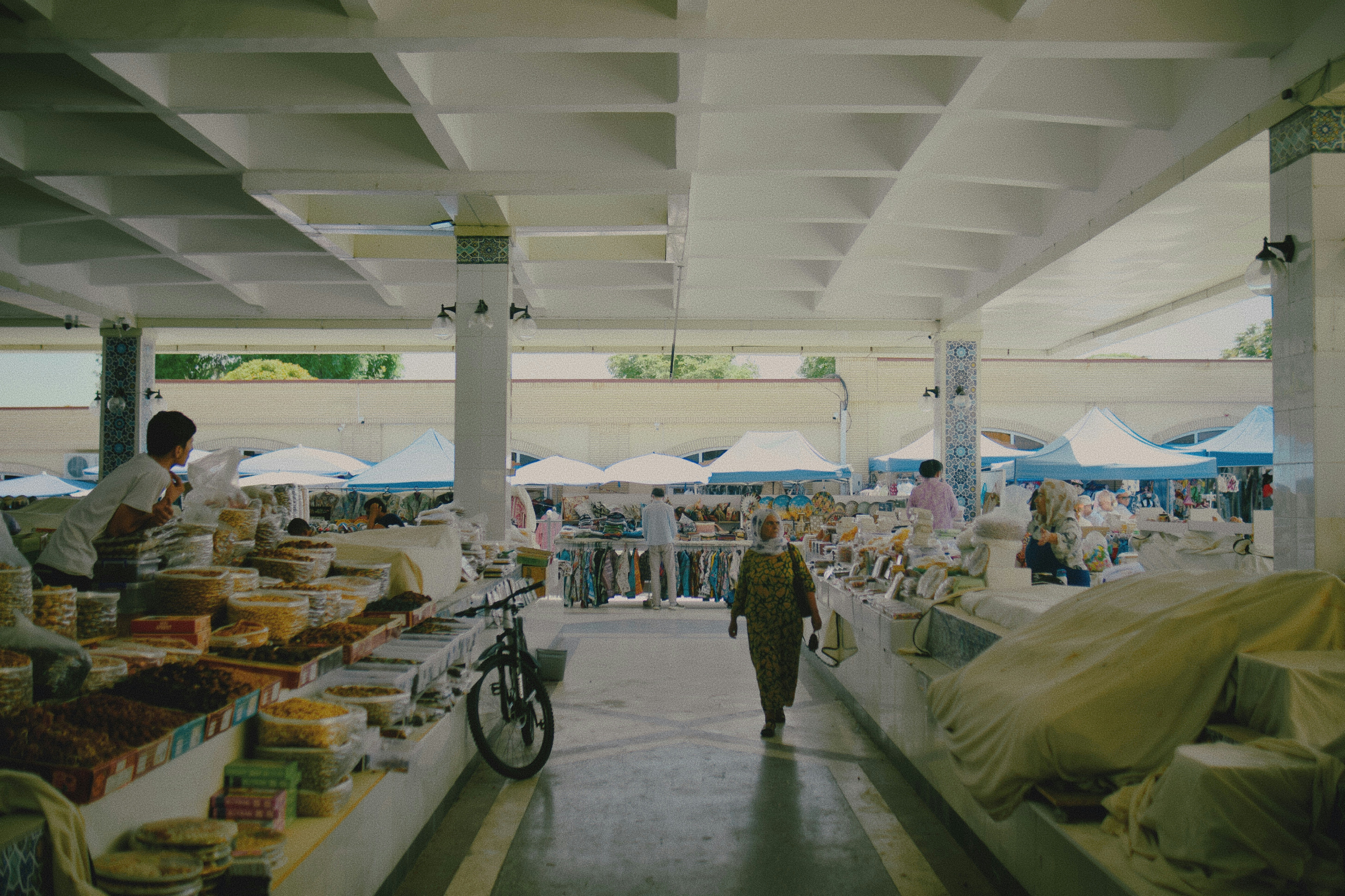Market Corridor: A Shopper Walks Amid Stalls Under White Canopies