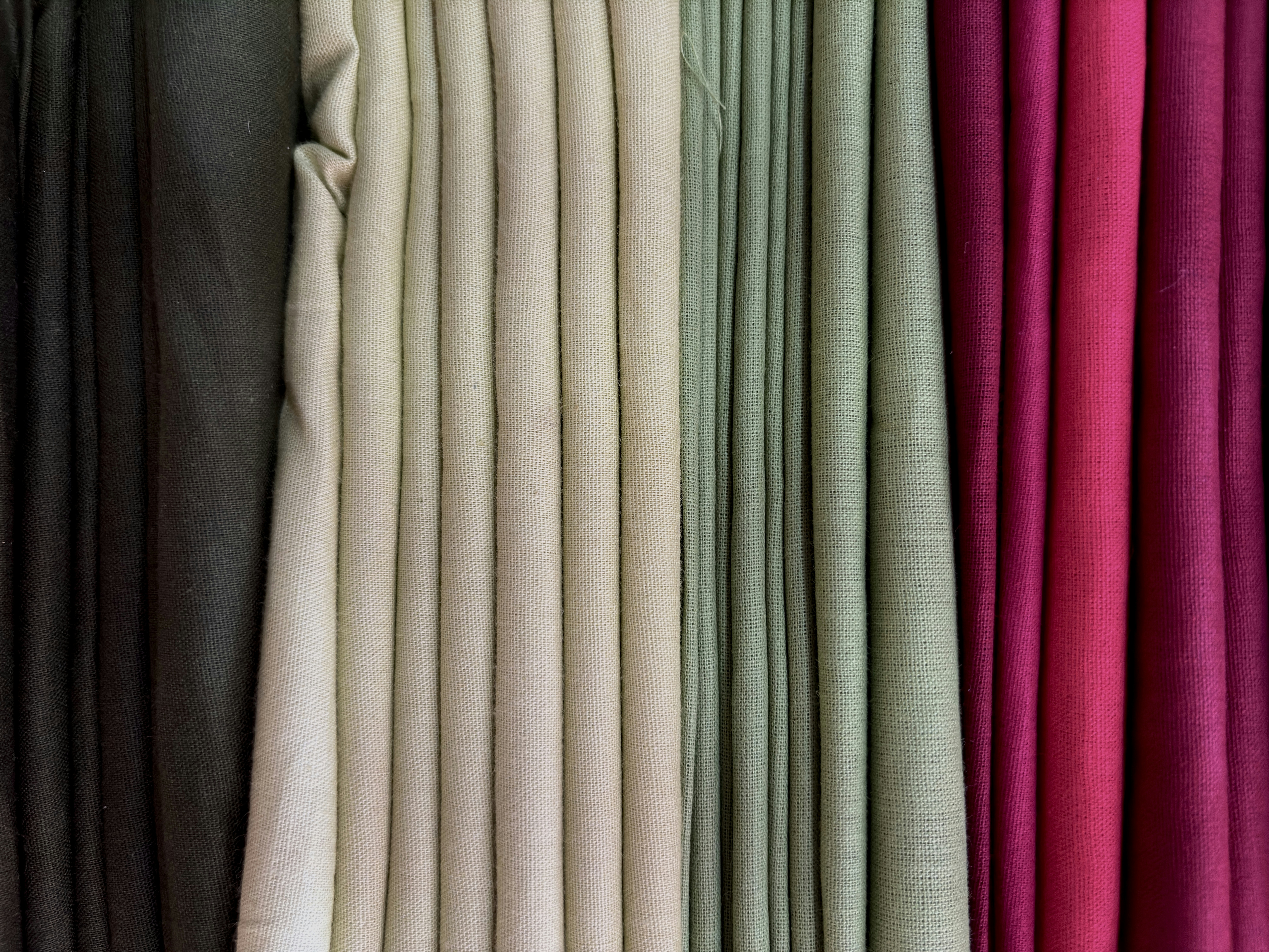 Rows of folded fabric in varying colors create soft vertical rhythm and texture, with a subtle gradient from dark to bright hues.