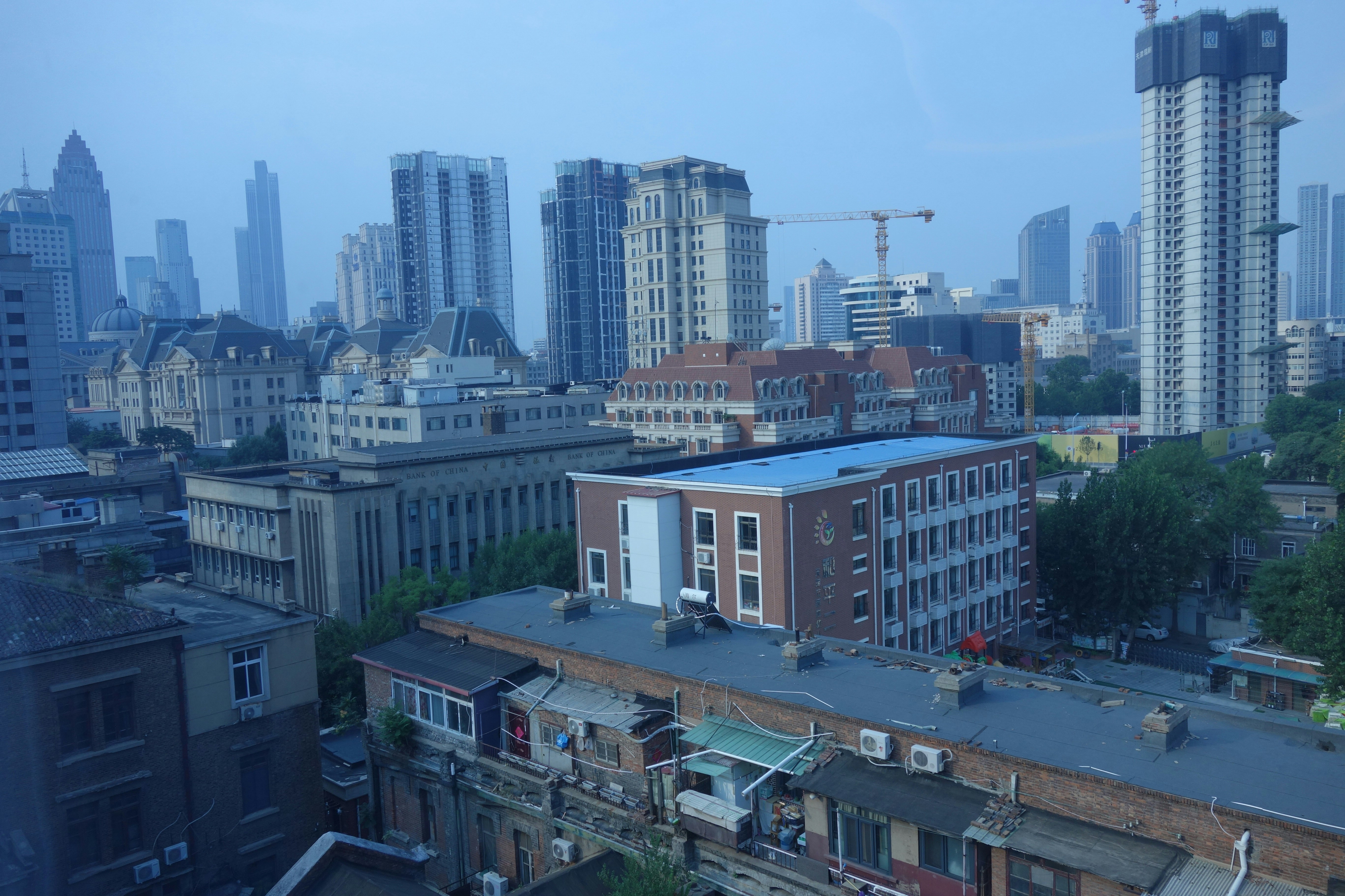 Urban rooftop view with mid-rise buildings in the foreground and a cluster of high-rises in the background during blue hour.