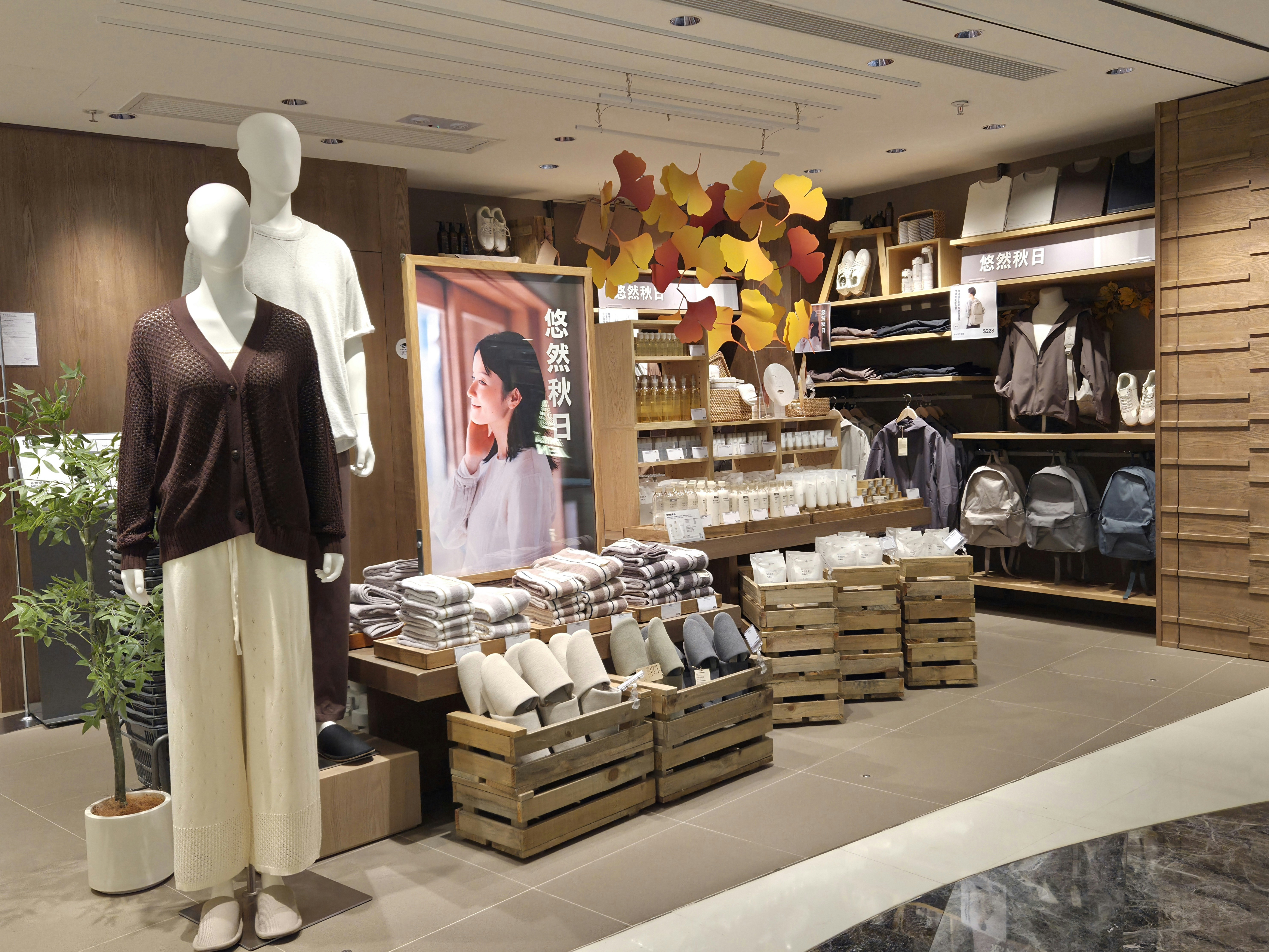 A retail clothing display with mannequins, shelves of folded garments, and wooden crates in a well-lit shop interior.