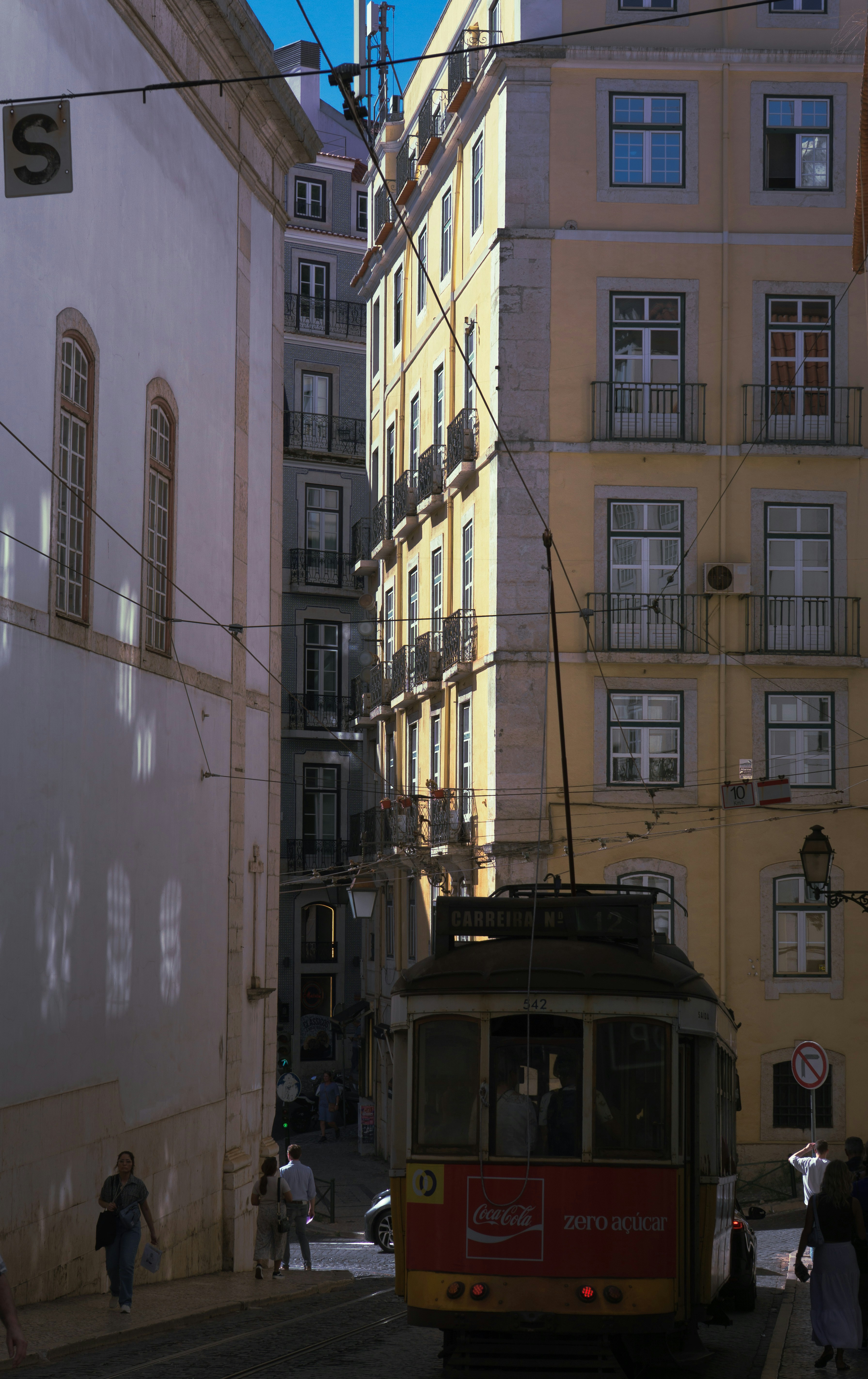 Yellow-tinted tram marching through a sunlit Lisbon alley