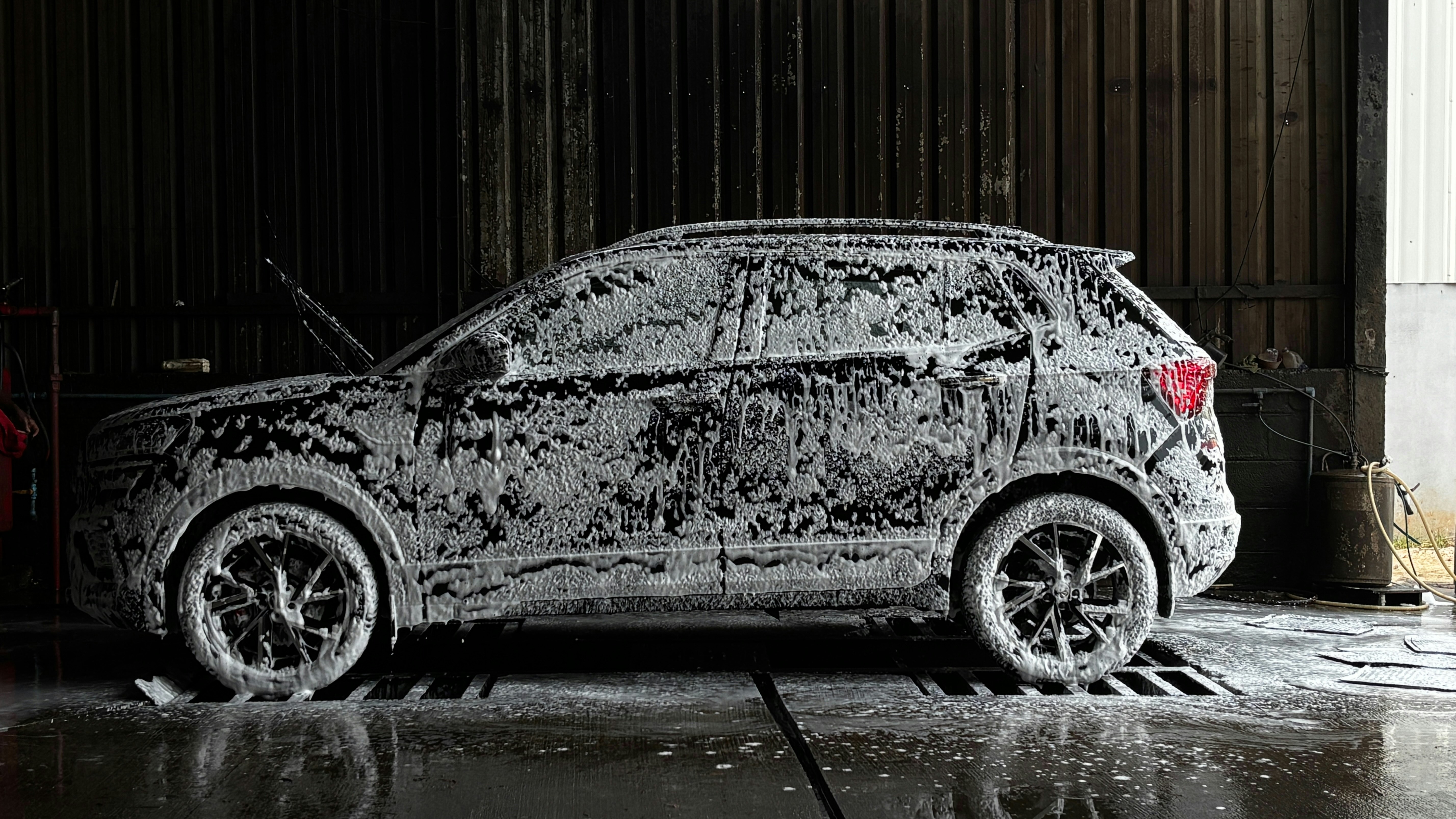 Snow-covered SUV parked in a dim wash bay, soap suds clinging to the body and wet floor reflecting light.