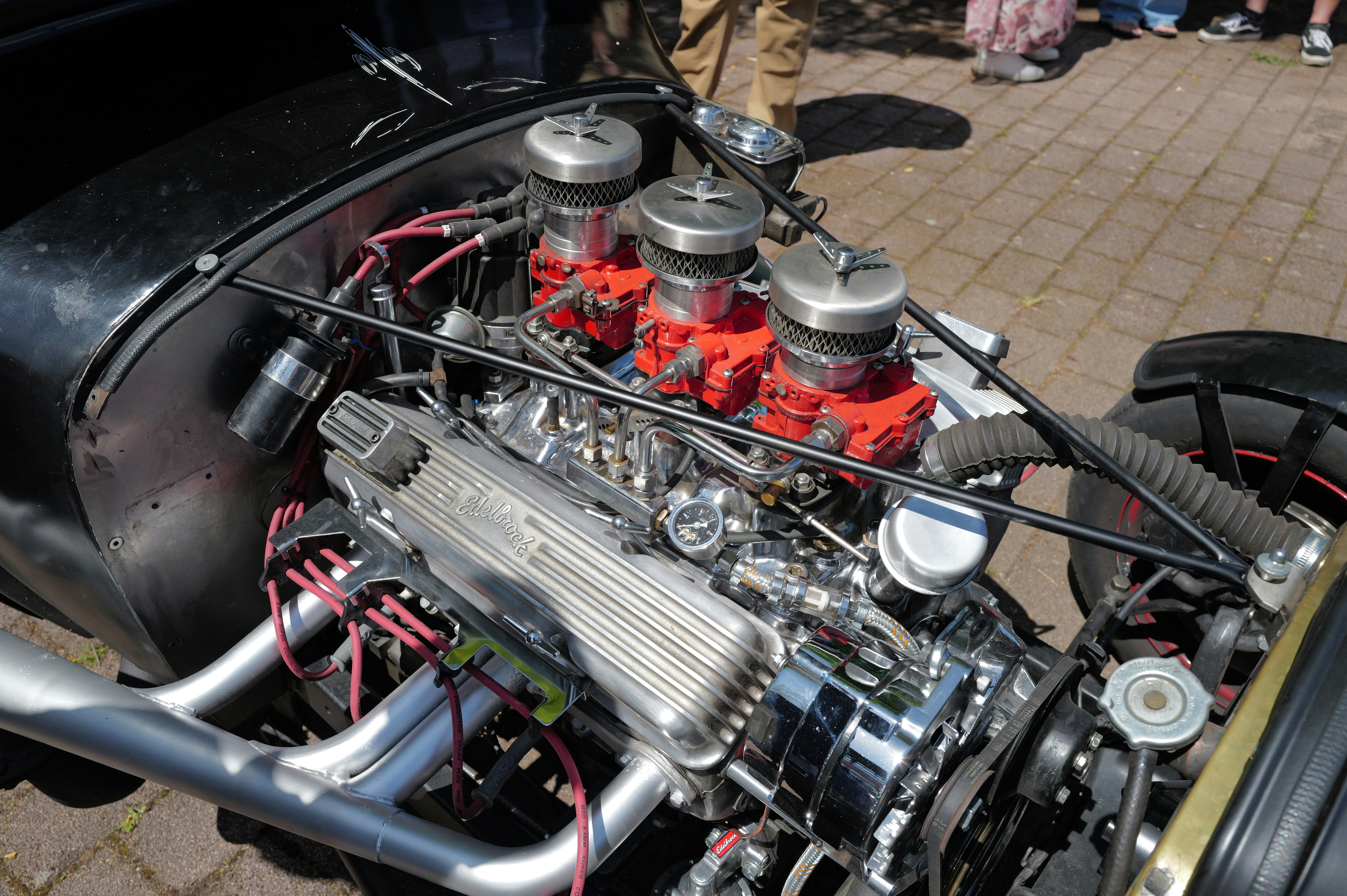 Close-up of a high-performance car engine with gleaming chrome, red carburetors, and intake manifolds, revealing intricate mechanical details and industrial precision.
