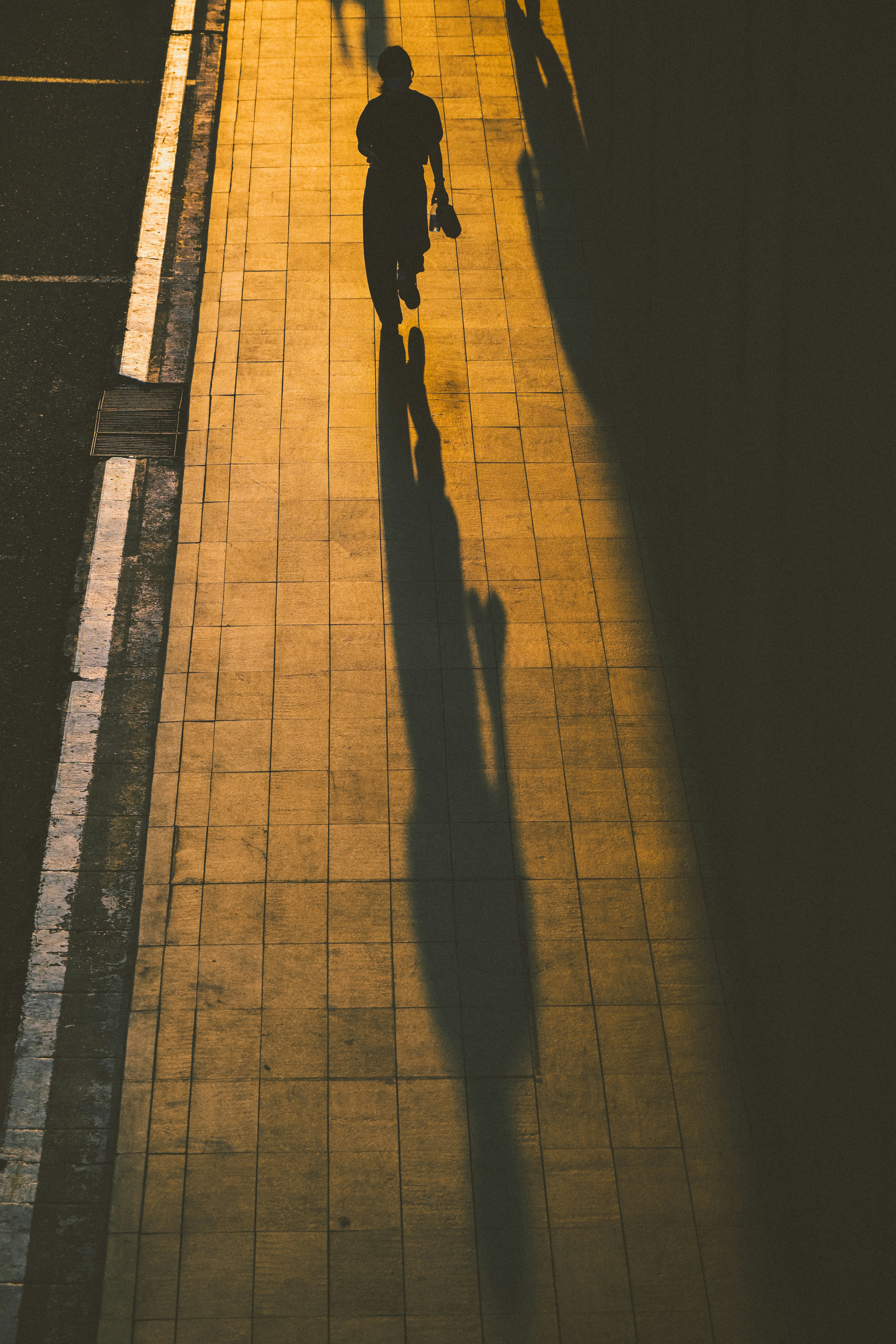Shadow on Yellow Tiles: A Lone Figure Walks the Sunlit Border