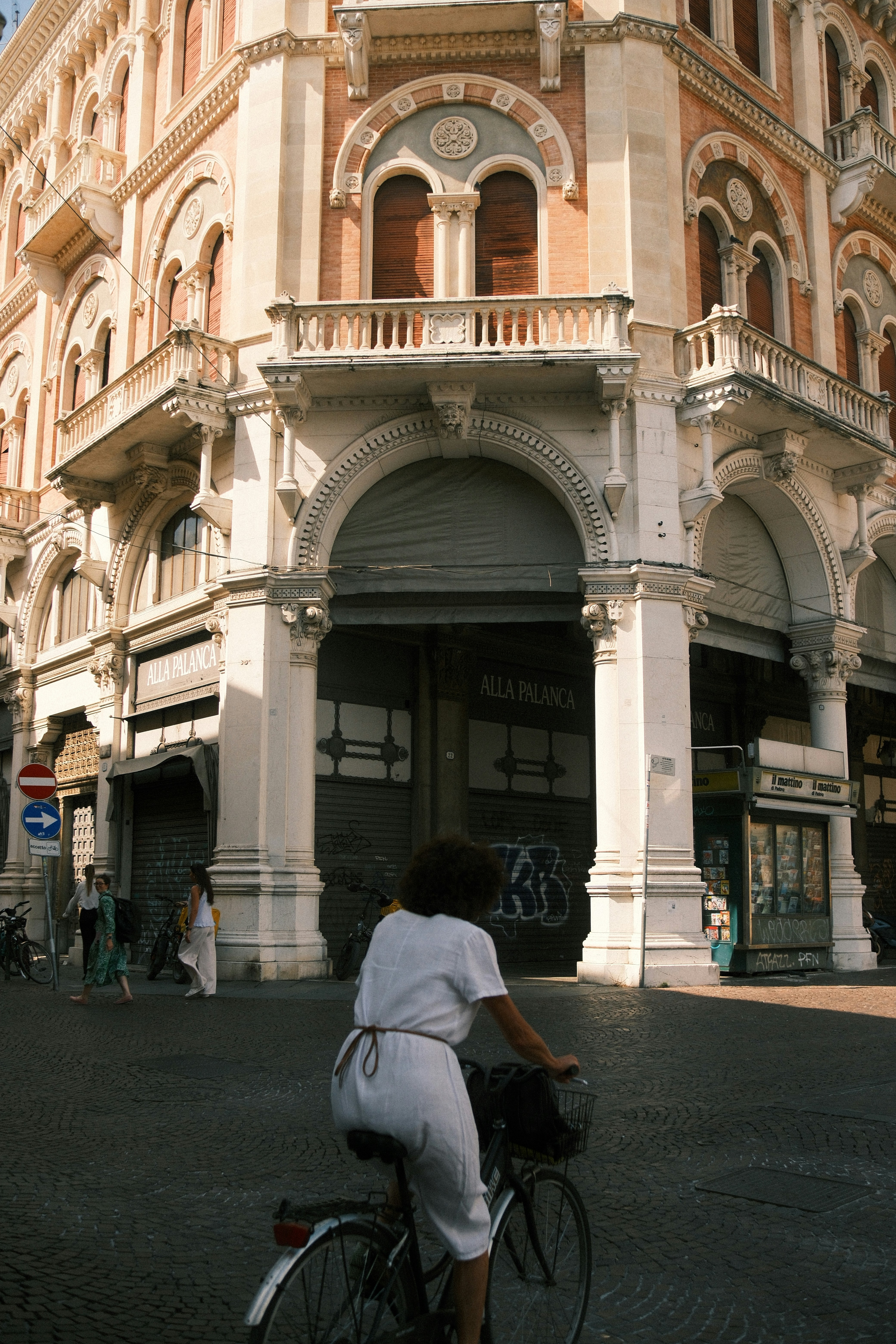 Cyclist in front of ornate arcade draped in Italian sunlight
