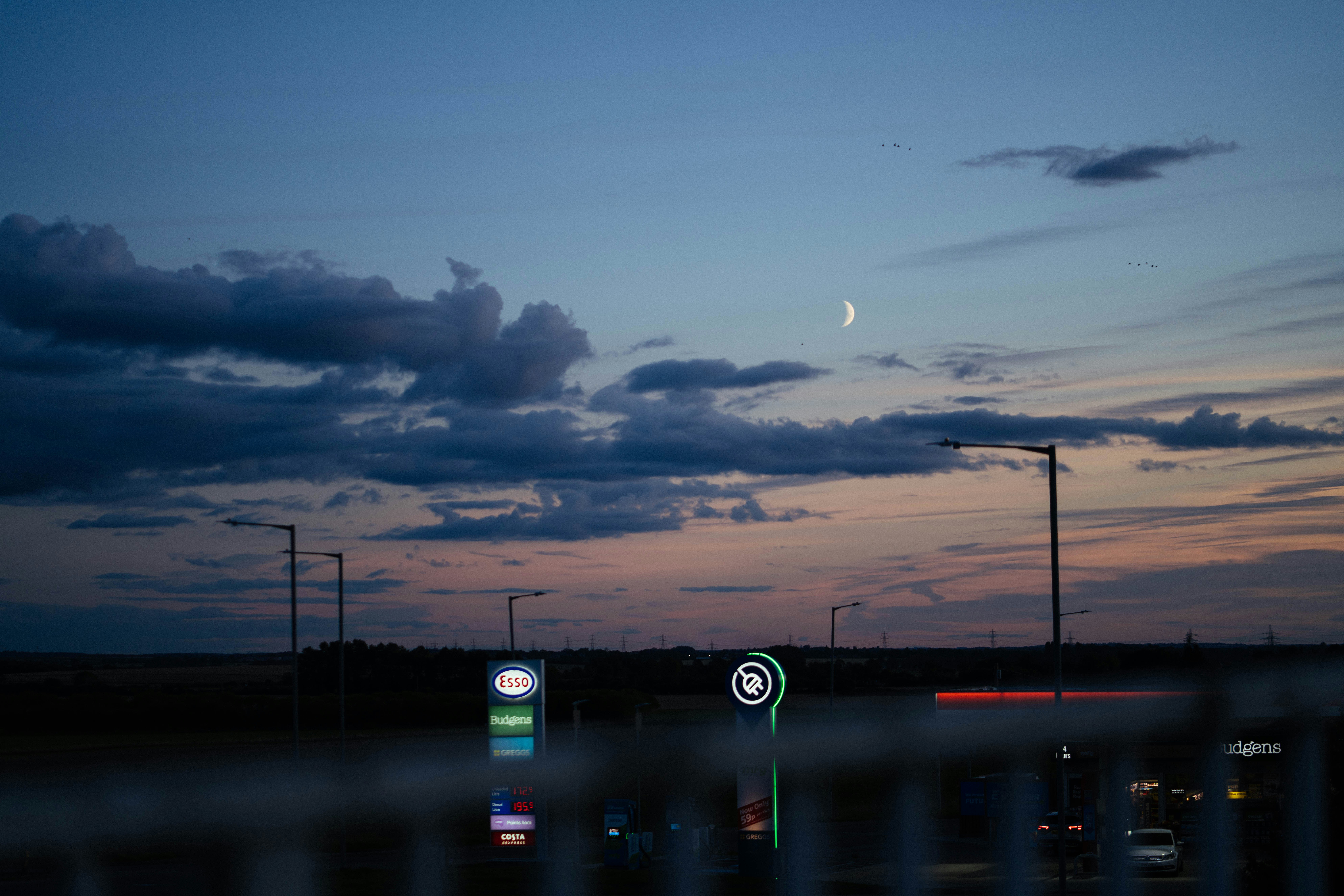 Dusk at the Quiet Edge: Crescent Moon over Neon Pumps