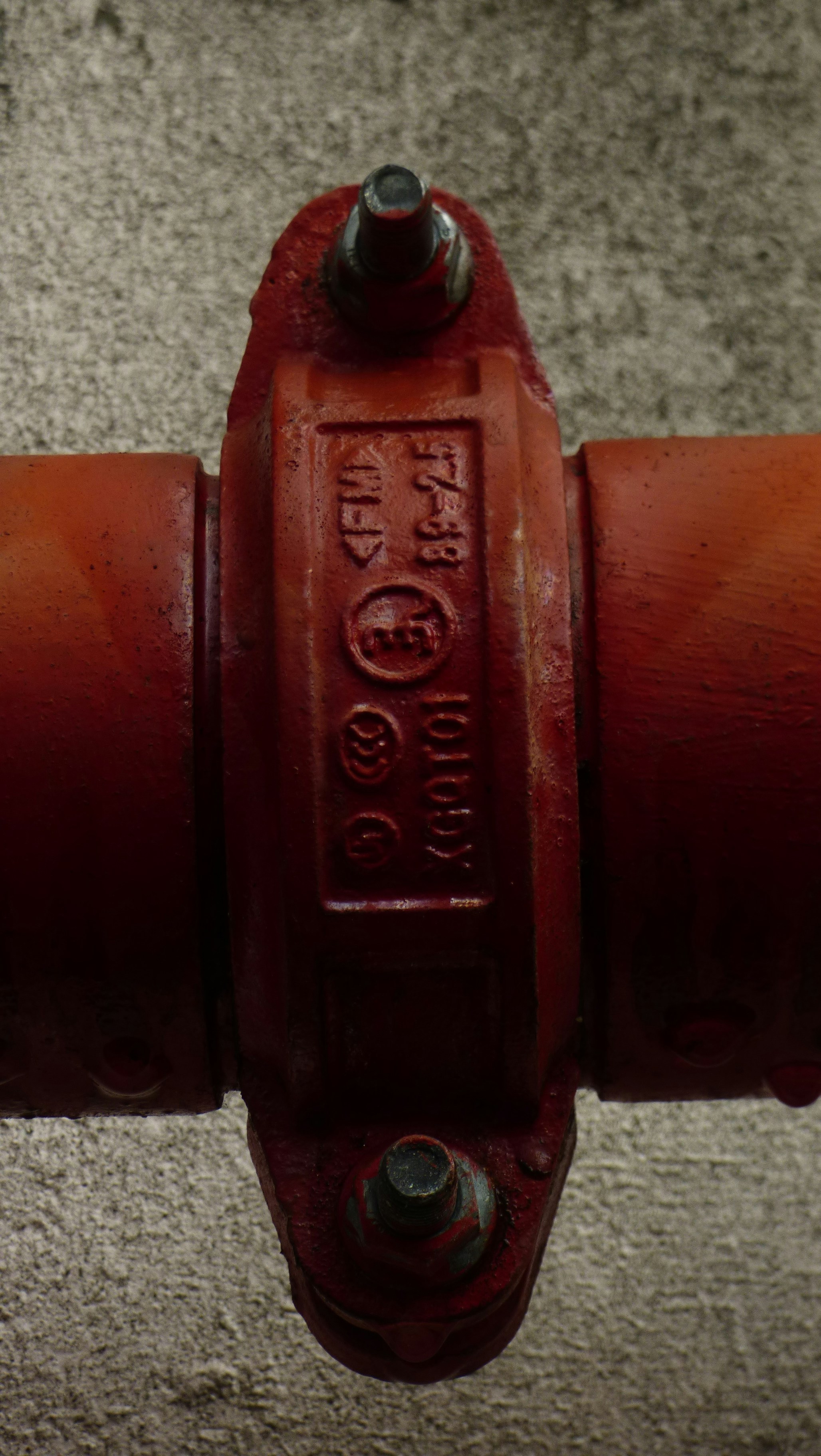 Red pipe clamp close-up: a weathered joint under gritty light