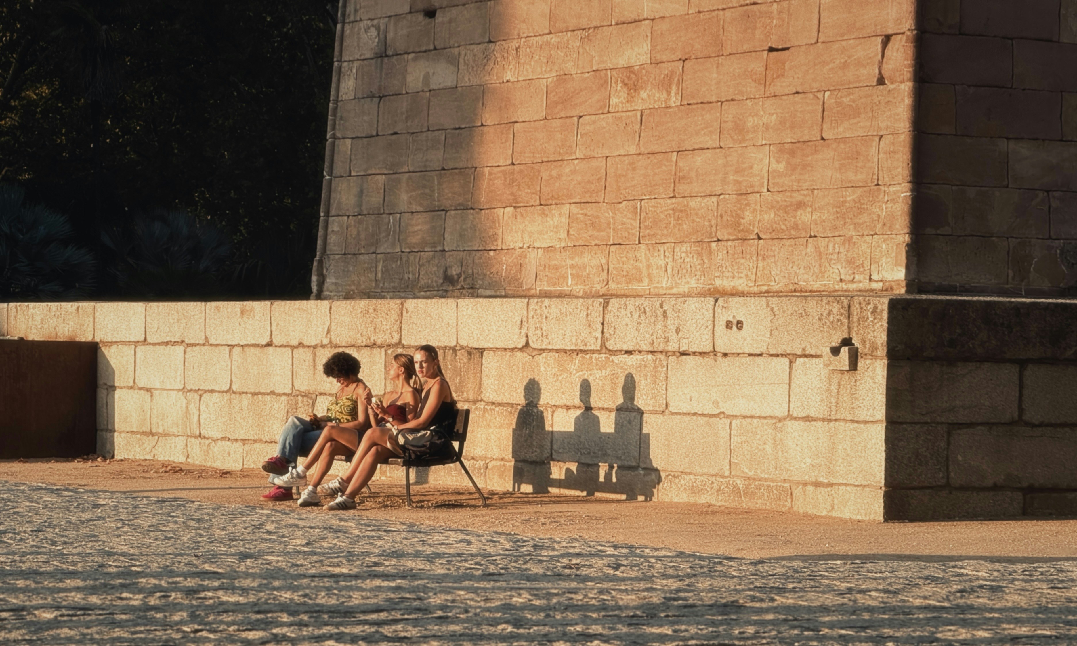Sunlit quiet by the stone wall: friends share a moment in shadow