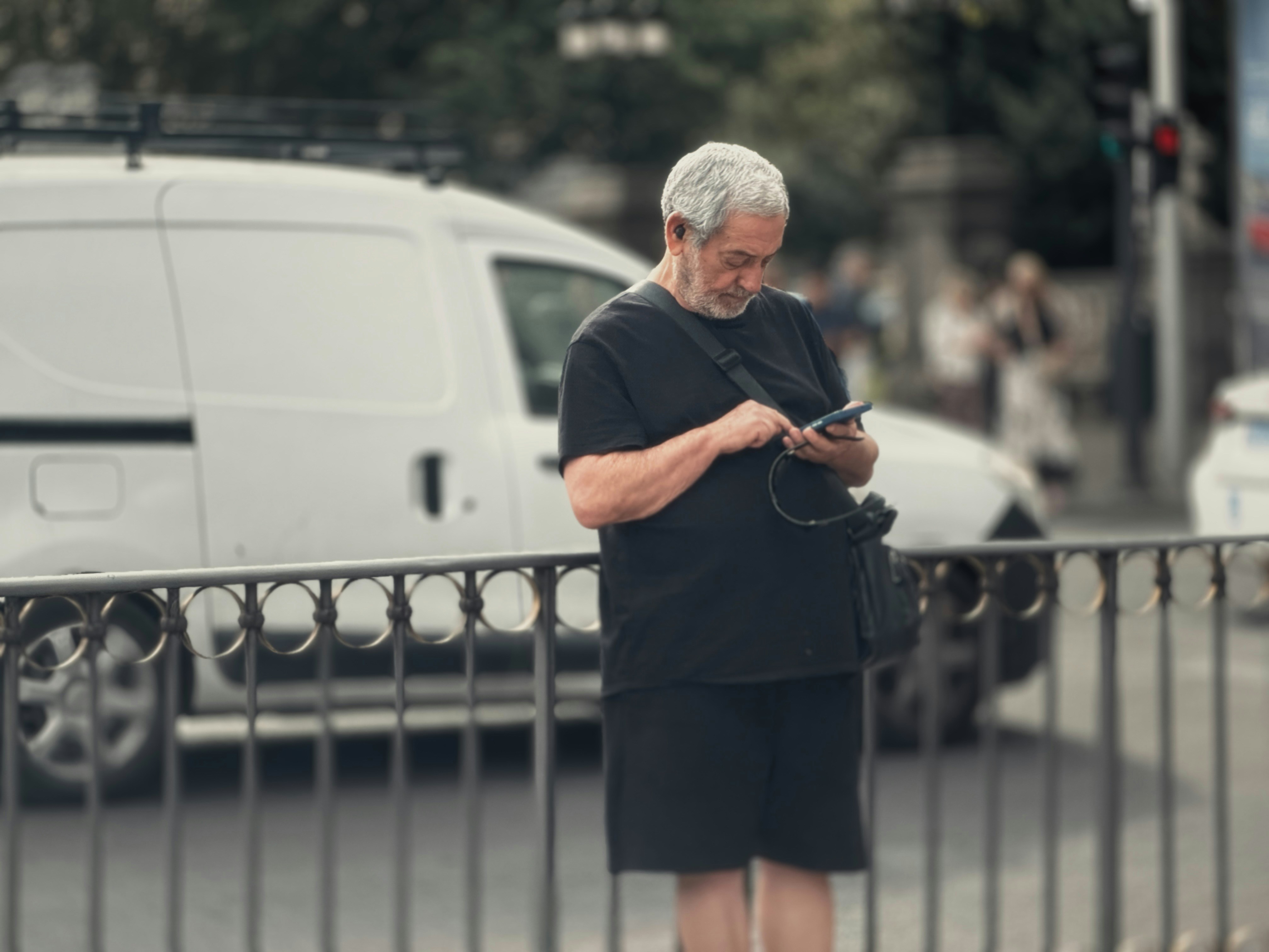 Man with White Beard Concentrates on Phone Amid Urban Drift