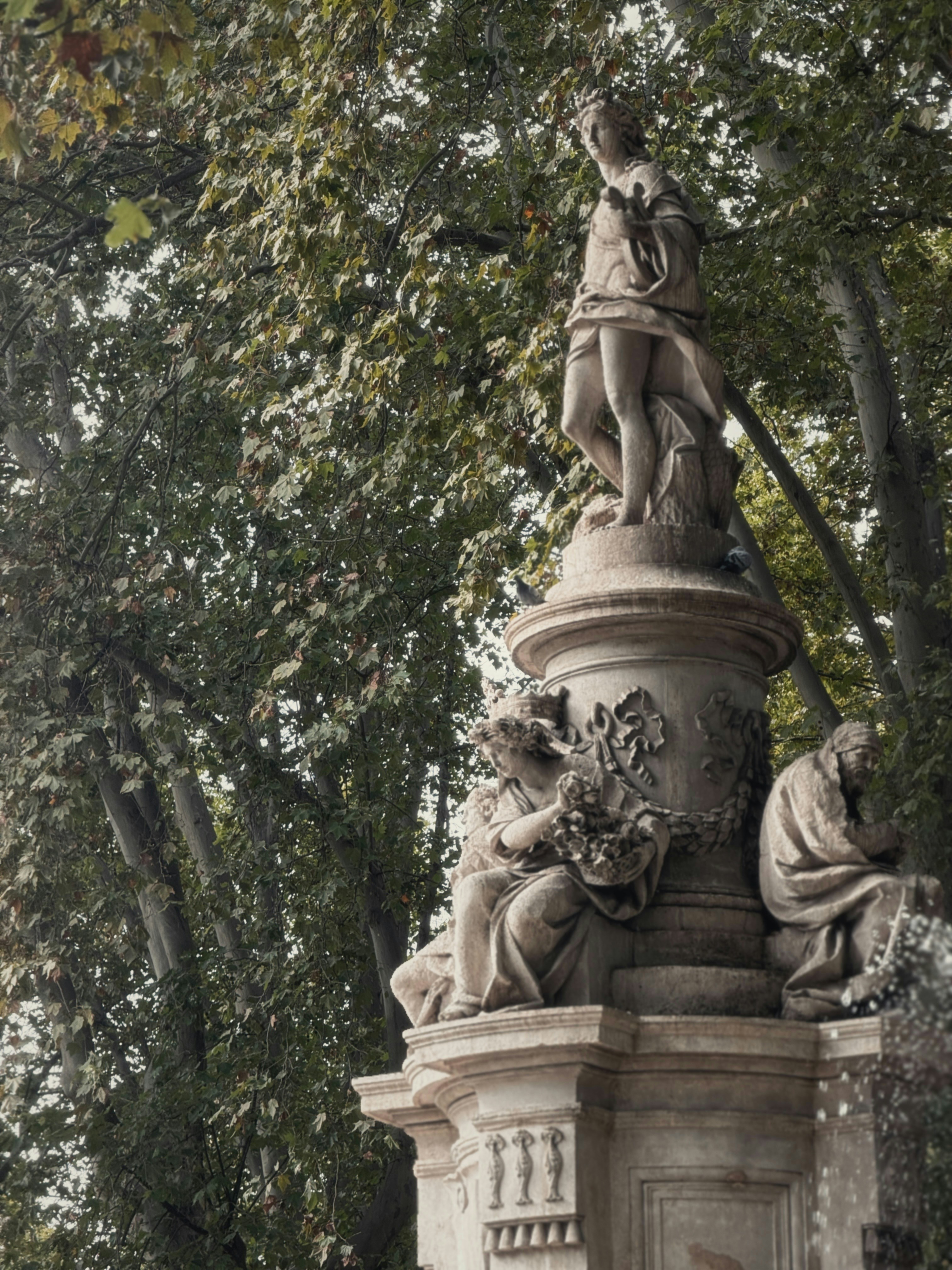 Statue atop a carved pedestal tucked among leafy branches